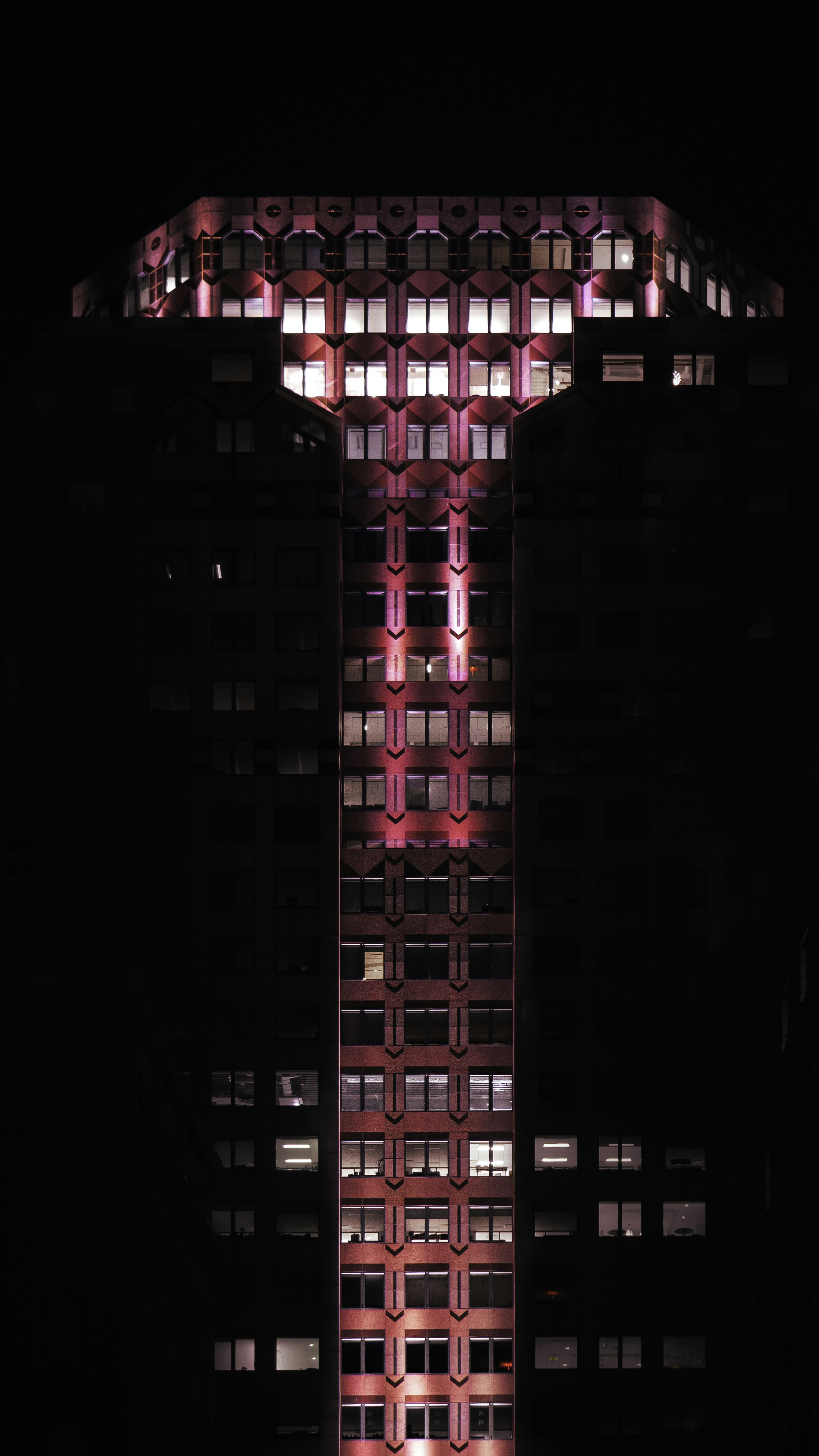Illuminated high-rise building showcasing geometric patterns and vibrant lighting against a night sky.