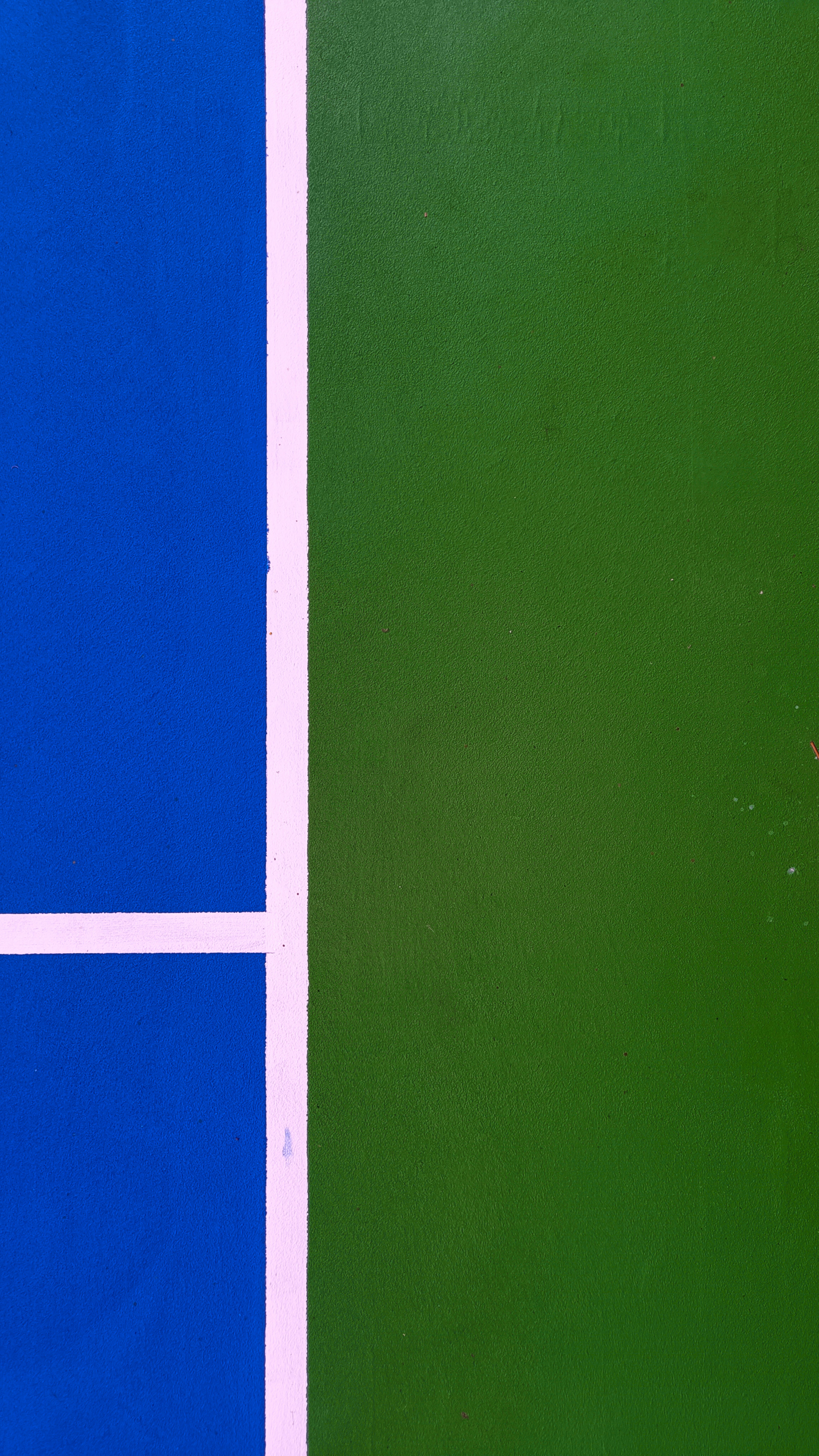 Color-blocked court surface with bold blue on the left and green on the right, separated by crisp white lines. A photograph emphasizing geometric division and clean edge work.