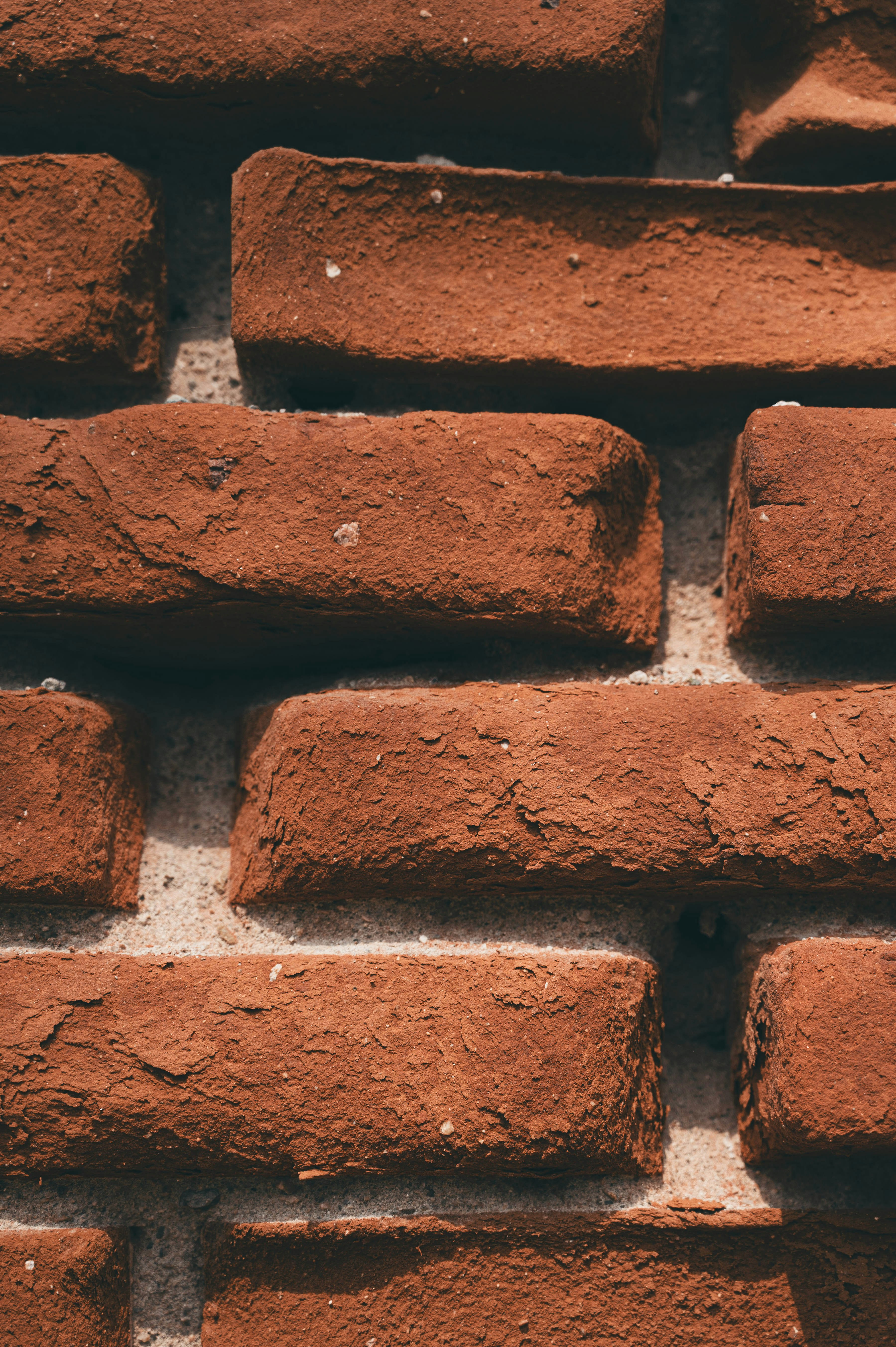 Close-up of a rustic brick wall showcasing the rich textures and colors of the clay bricks. The arrangement highlights the craftsmanship and natural imperfections of the materials.
