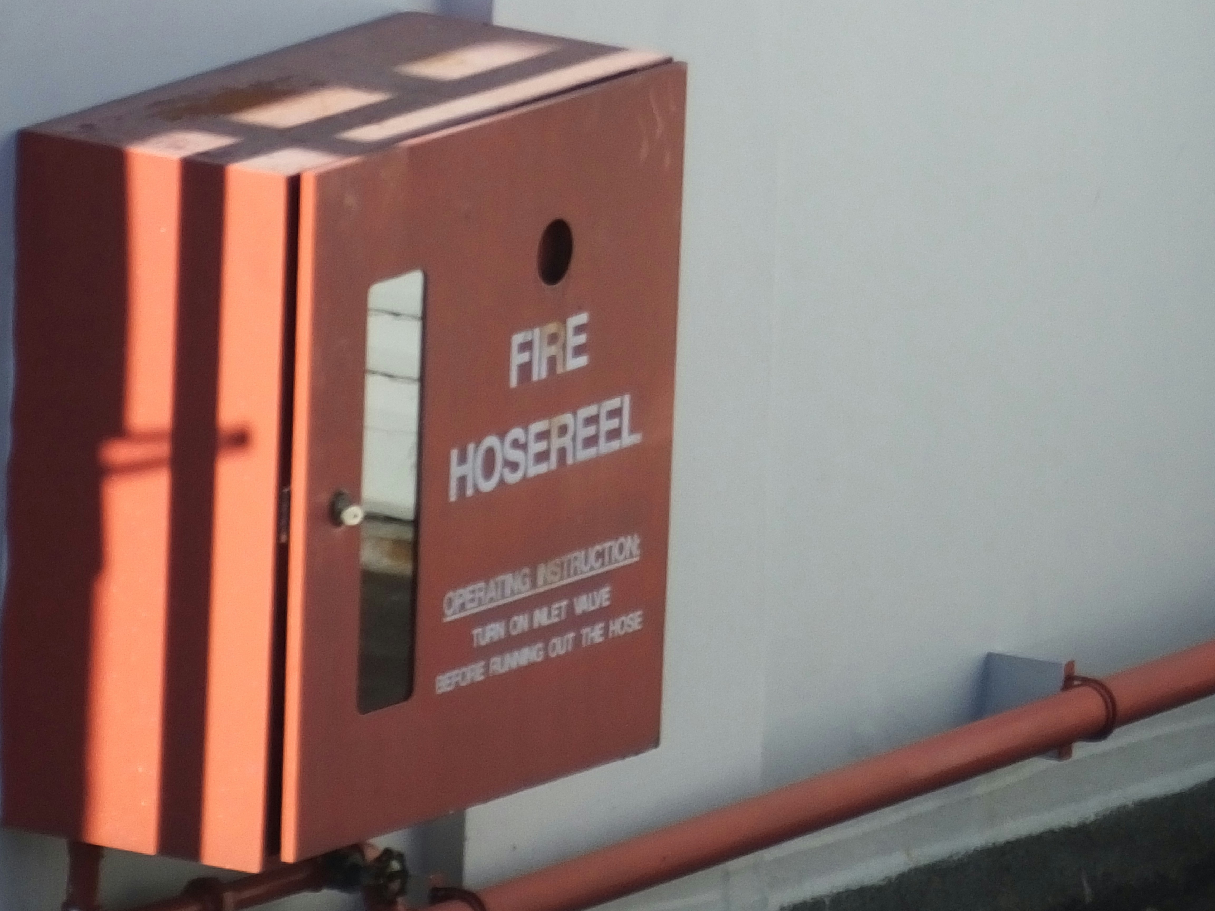 Bright red fire hosereel cabinet mounted on a wall, featuring clear operational instructions for emergency use.