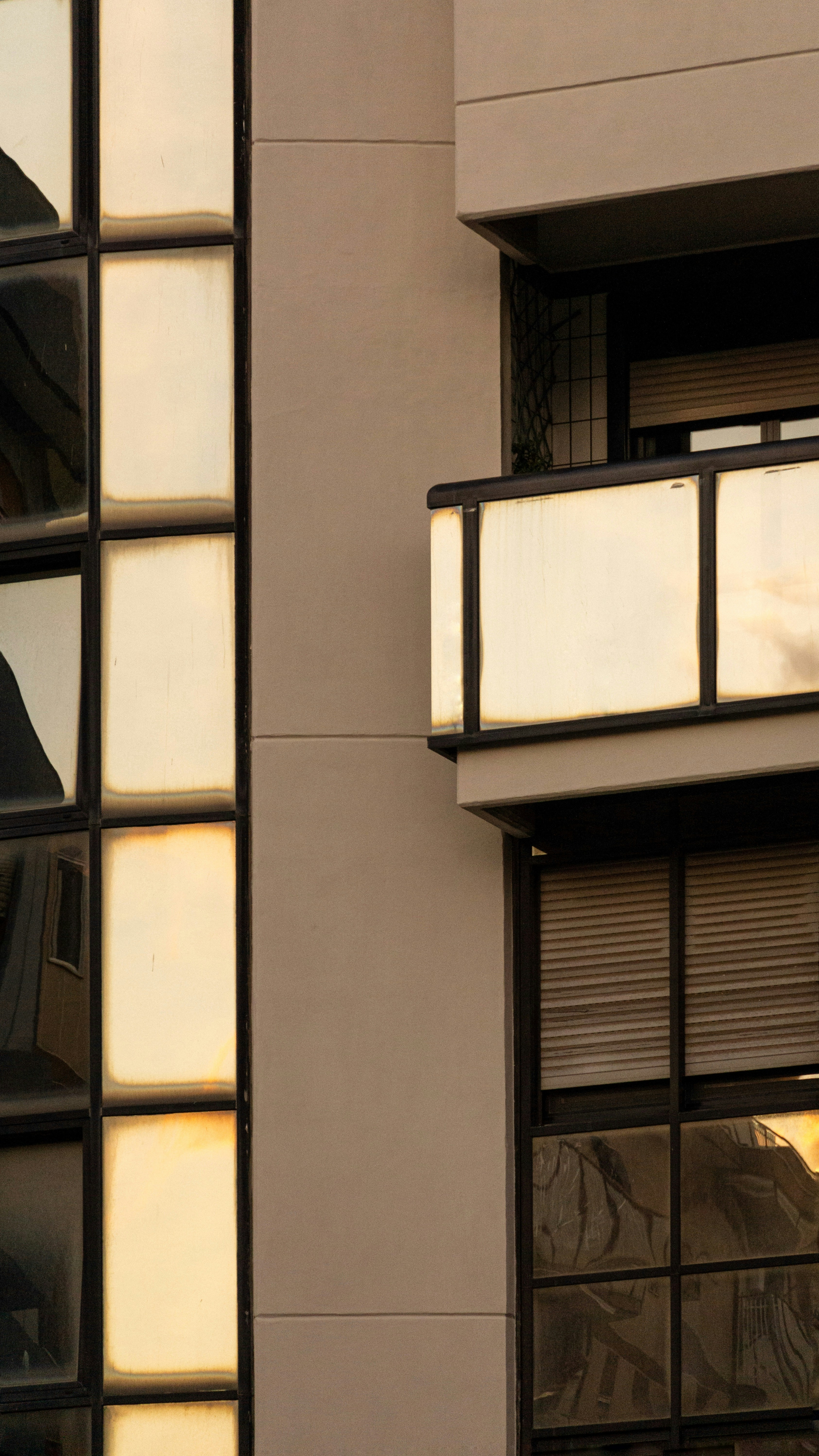 Close-up of a building facade showcasing reflective glass panels and a balcony, highlighting the interplay of architecture and light.
