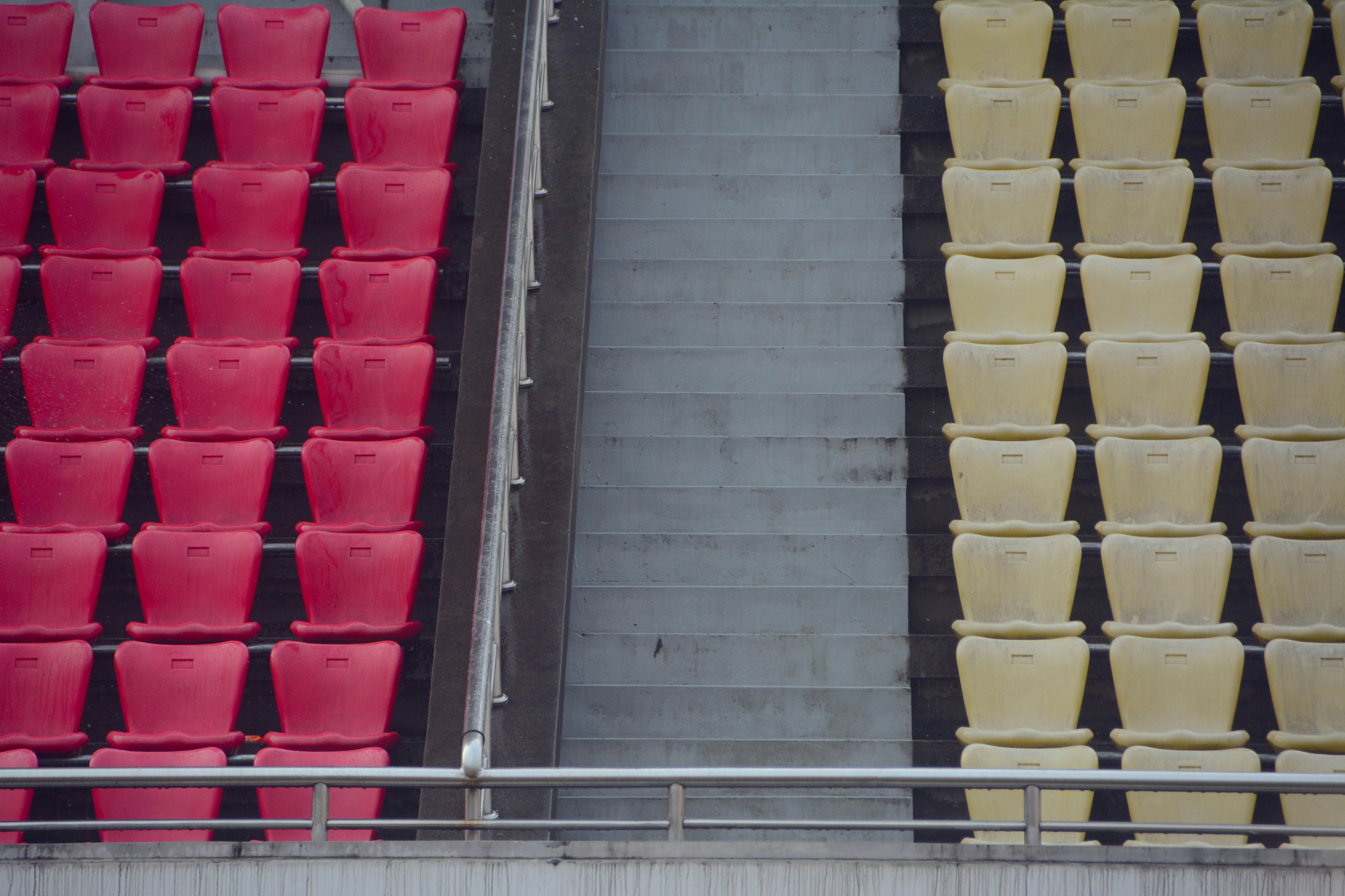 Rows of empty stadium seats in alternating colors of red and yellow, creating a striking visual contrast against a muted background.