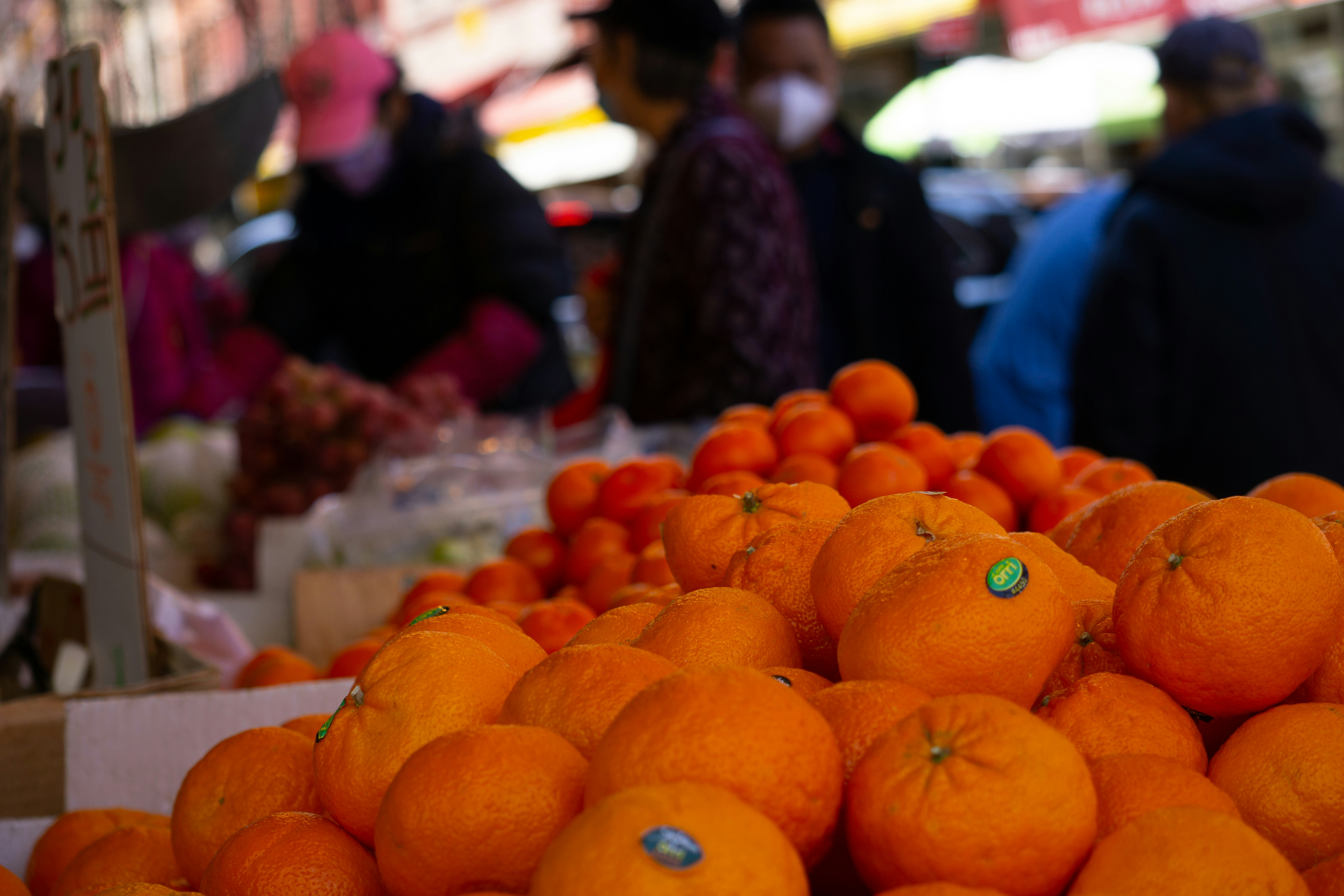 Vibrant display of oranges in a bustling market, with blurred figures of shoppers in the background. 