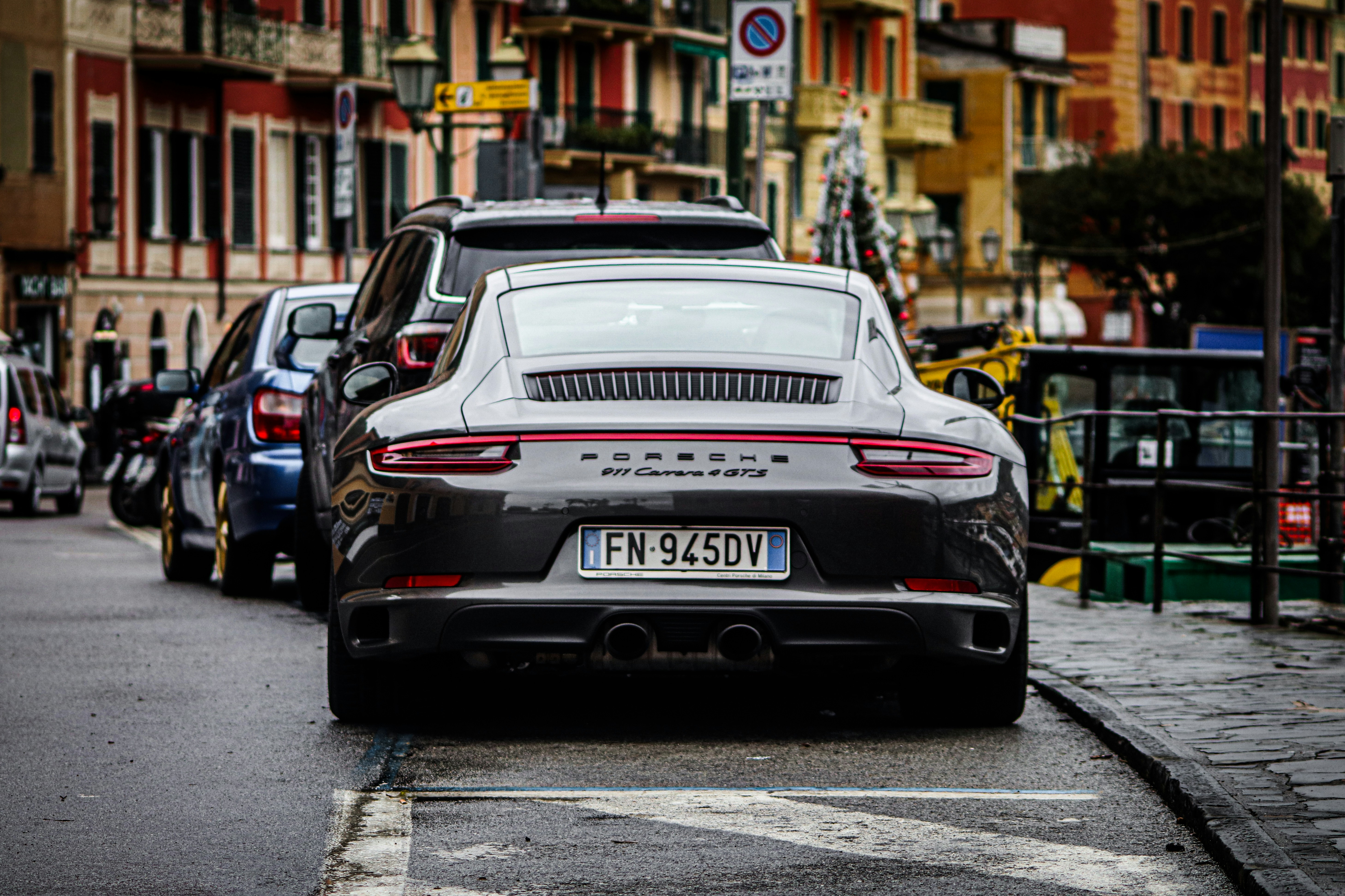 Sleek Porsche 911 Carrera S parked on a bustling city street, showcasing its distinctive rear design against a vibrant urban backdrop.