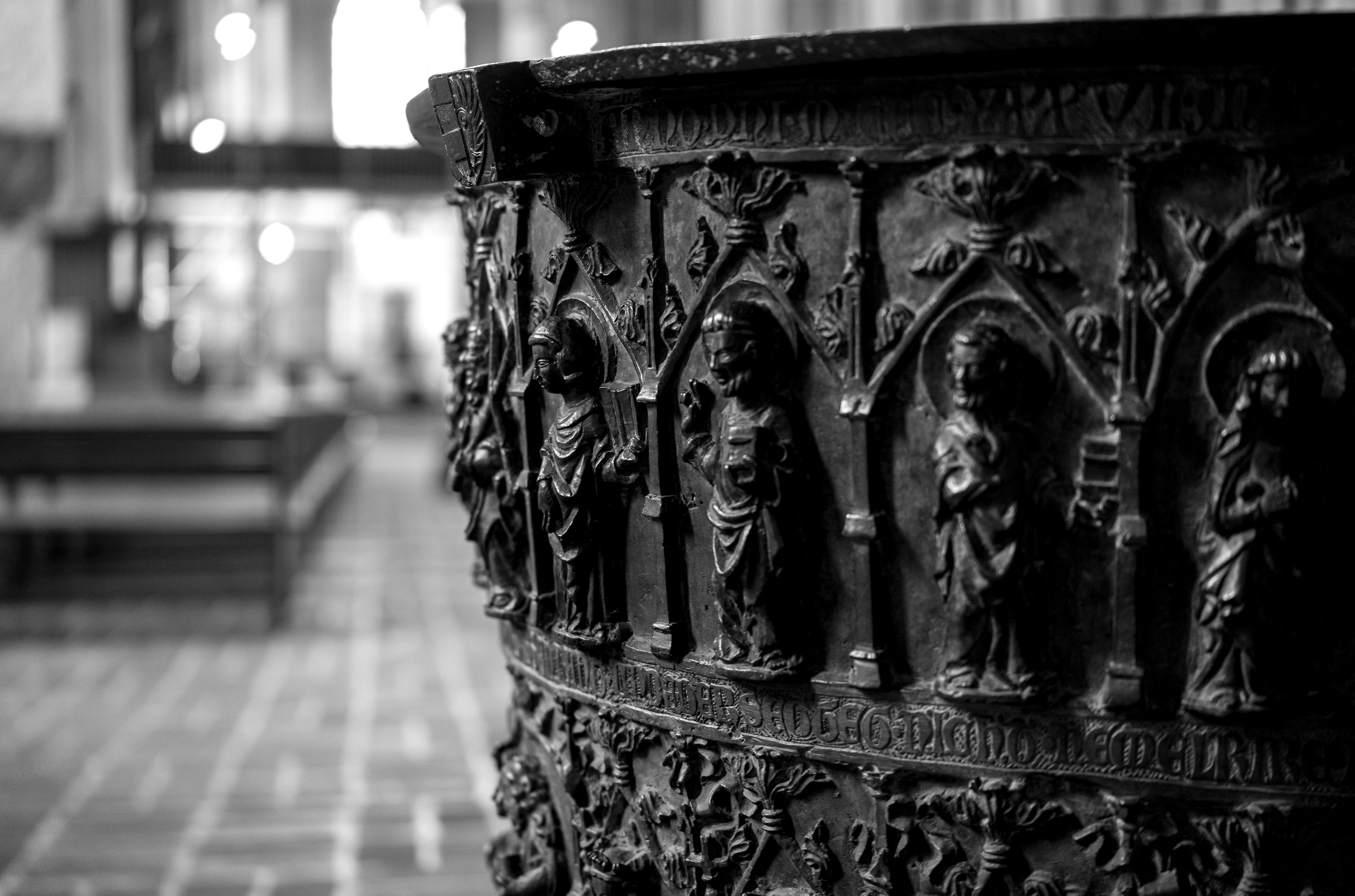 Detailed stone carvings on a baptismal font in a dimly lit church interior.