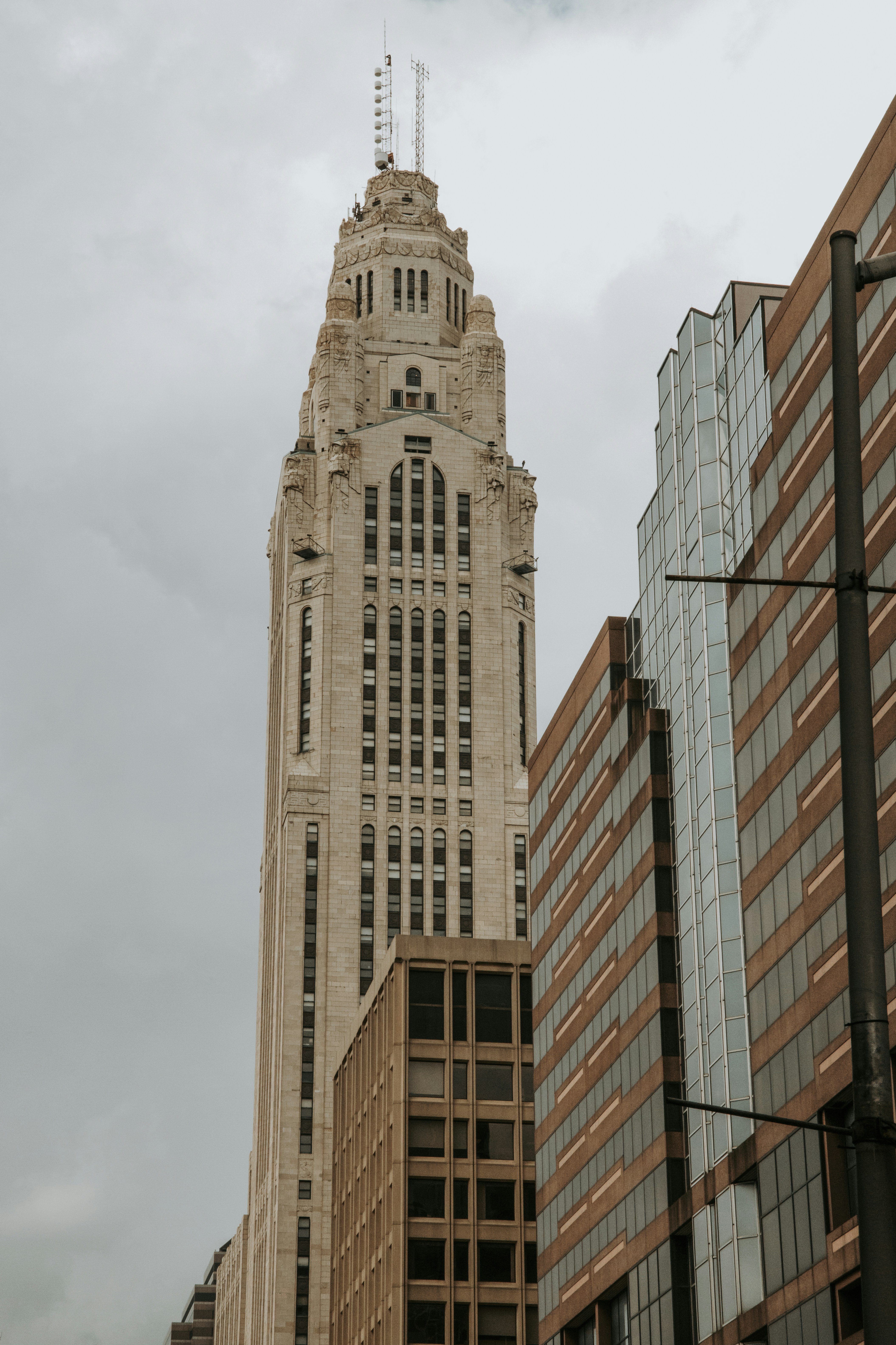 Art Deco skyscraper rising majestically above modern structures in an urban landscape under a cloudy sky.
