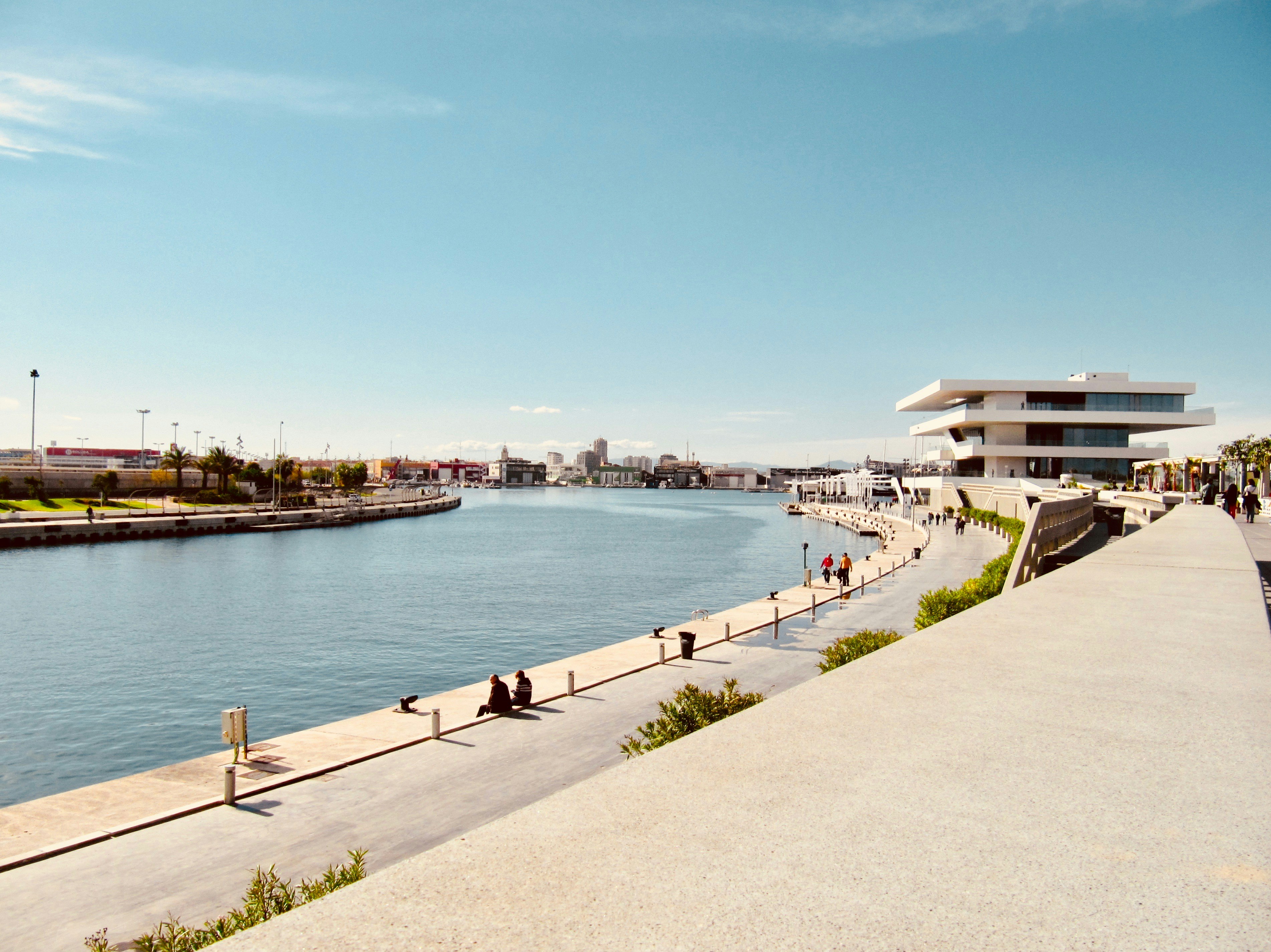 Curved riverside walkway with a modern building and blue sky.