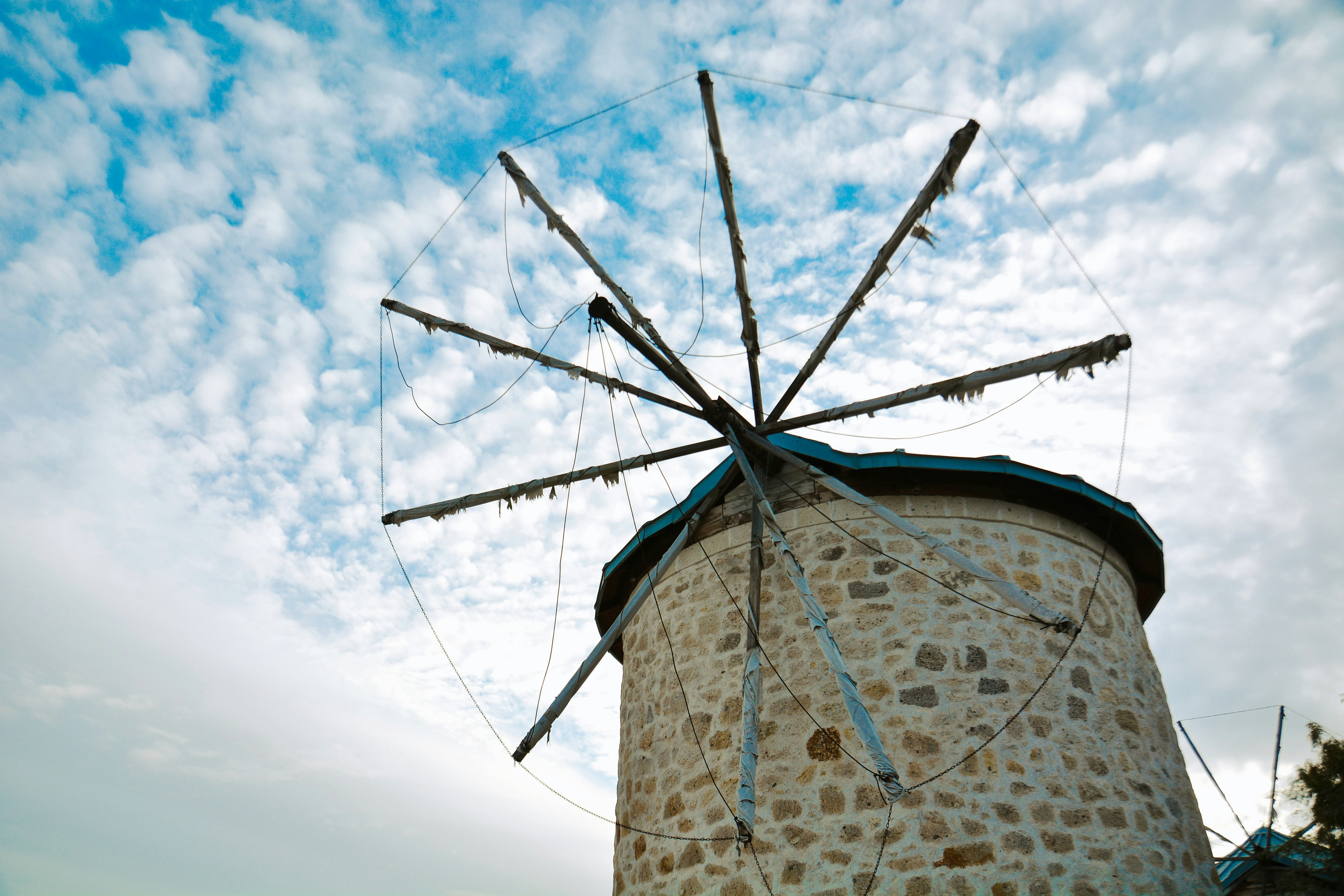 Historic windmill with a weathered stone base and a skeletal wheel against a cloudy sky.