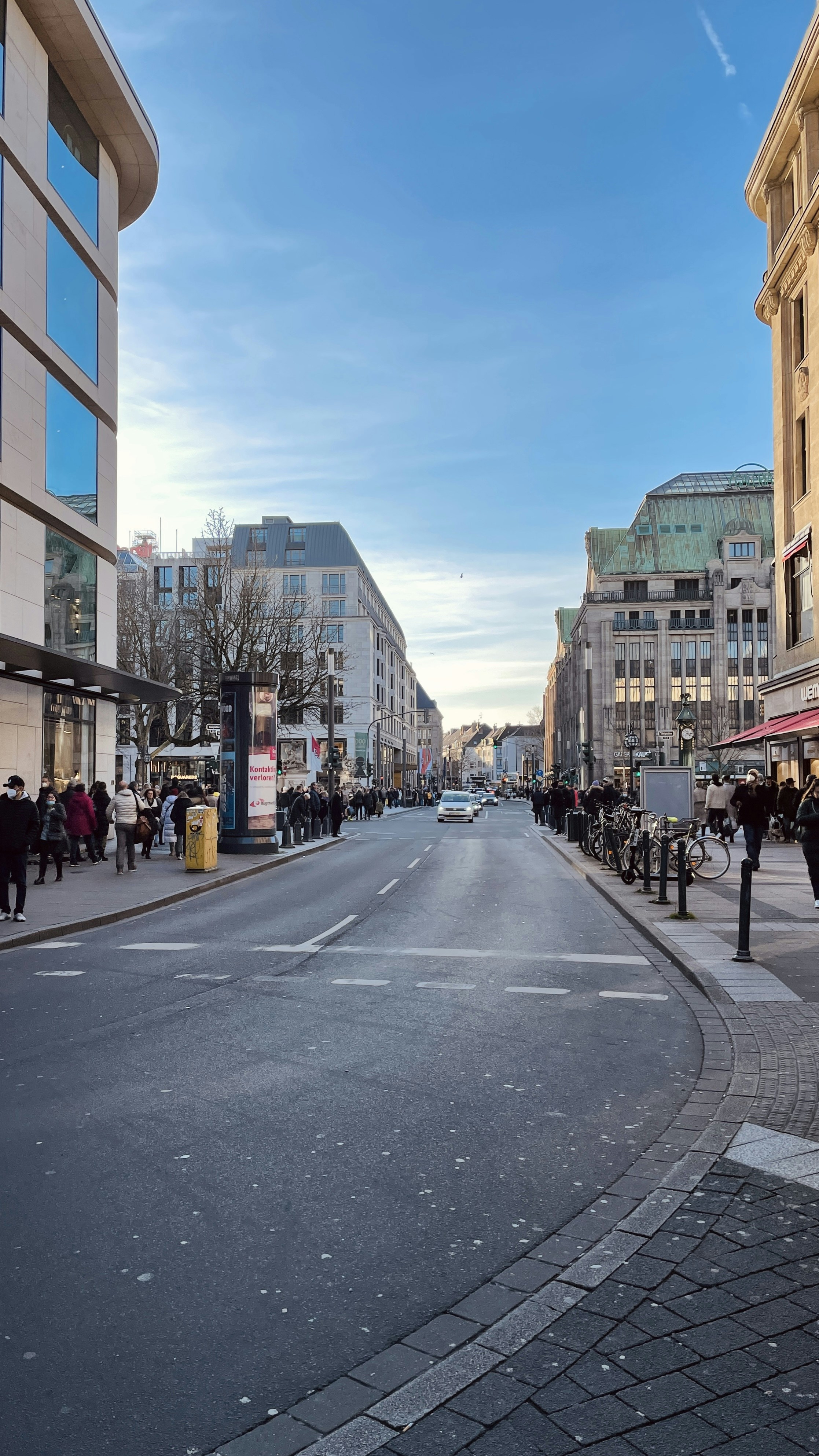 Bustling city street lined with shops and pedestrians, framed by modern architecture under a clear blue sky.