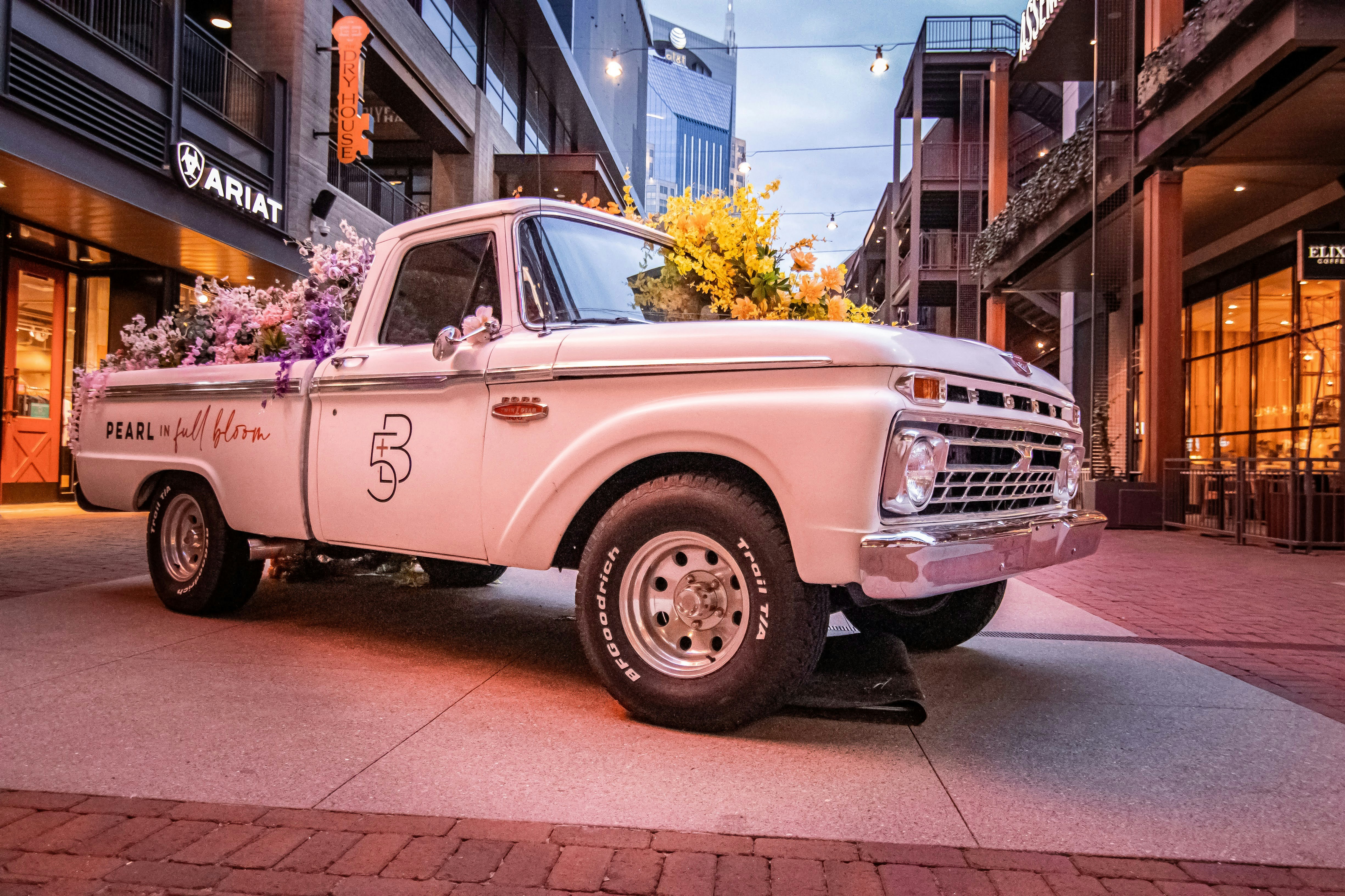 Classic white pickup truck adorned with flowers parked in a modern city street at twilight.