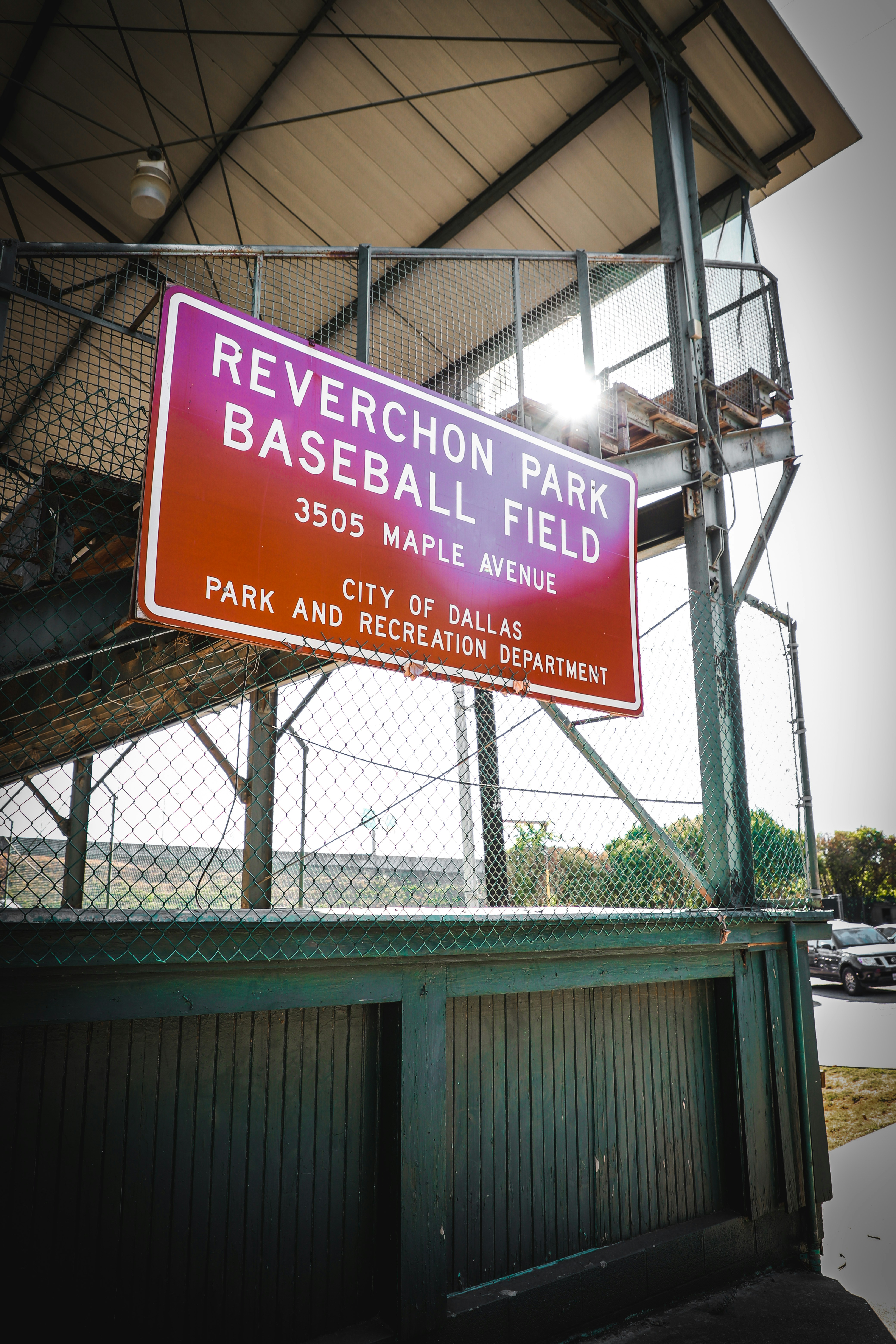 Sunlit Reverchon Park Baseball Field Sign: Chain-Link Frame and Urban Backdrop
