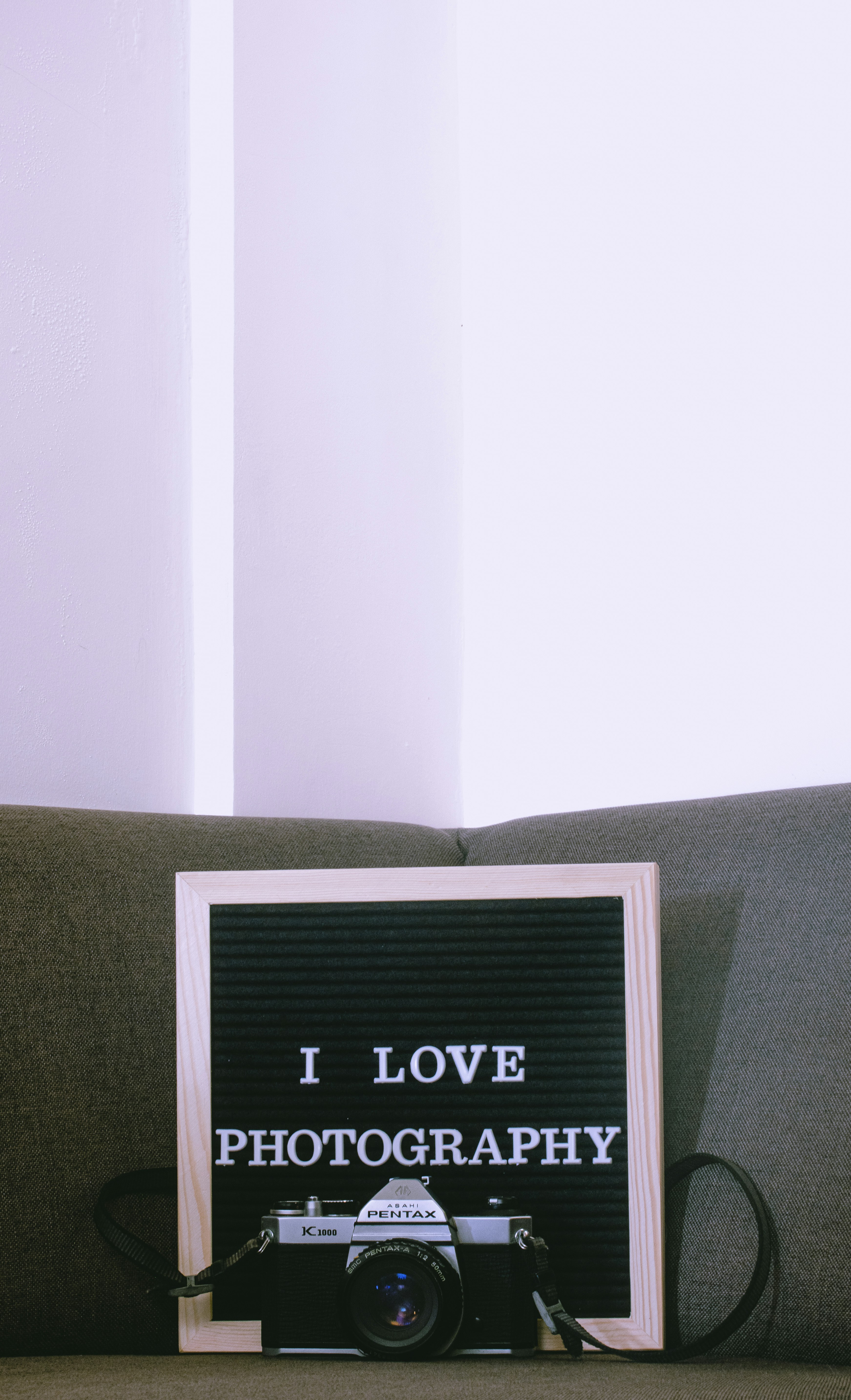 Soft Light, Vintage Gear: A Pentax on a Couch Beneath a Minimal Sign