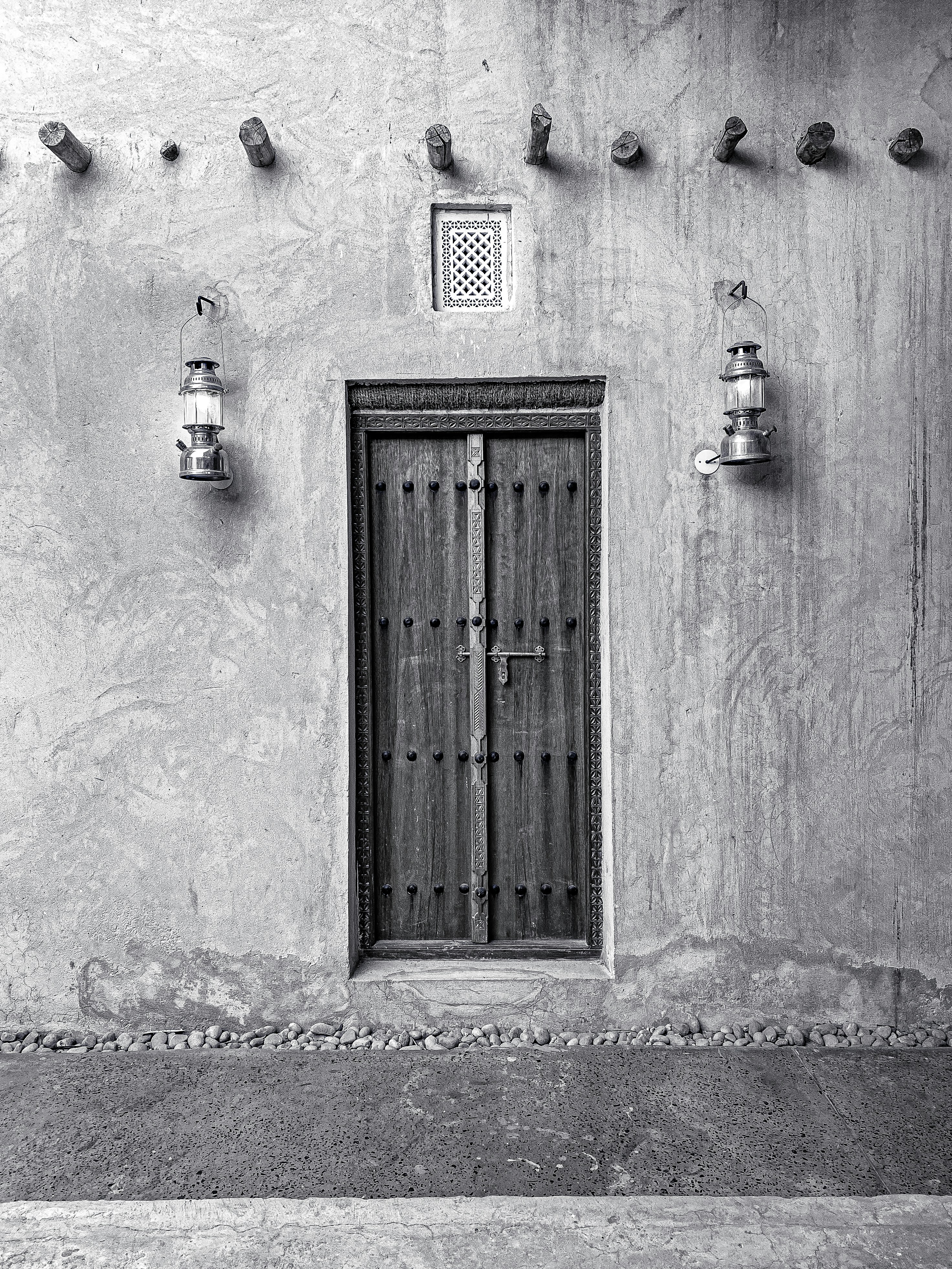Intricately carved wooden door framed by vintage lanterns against a textured wall. The scene evokes a sense of nostalgia and cultural heritage.