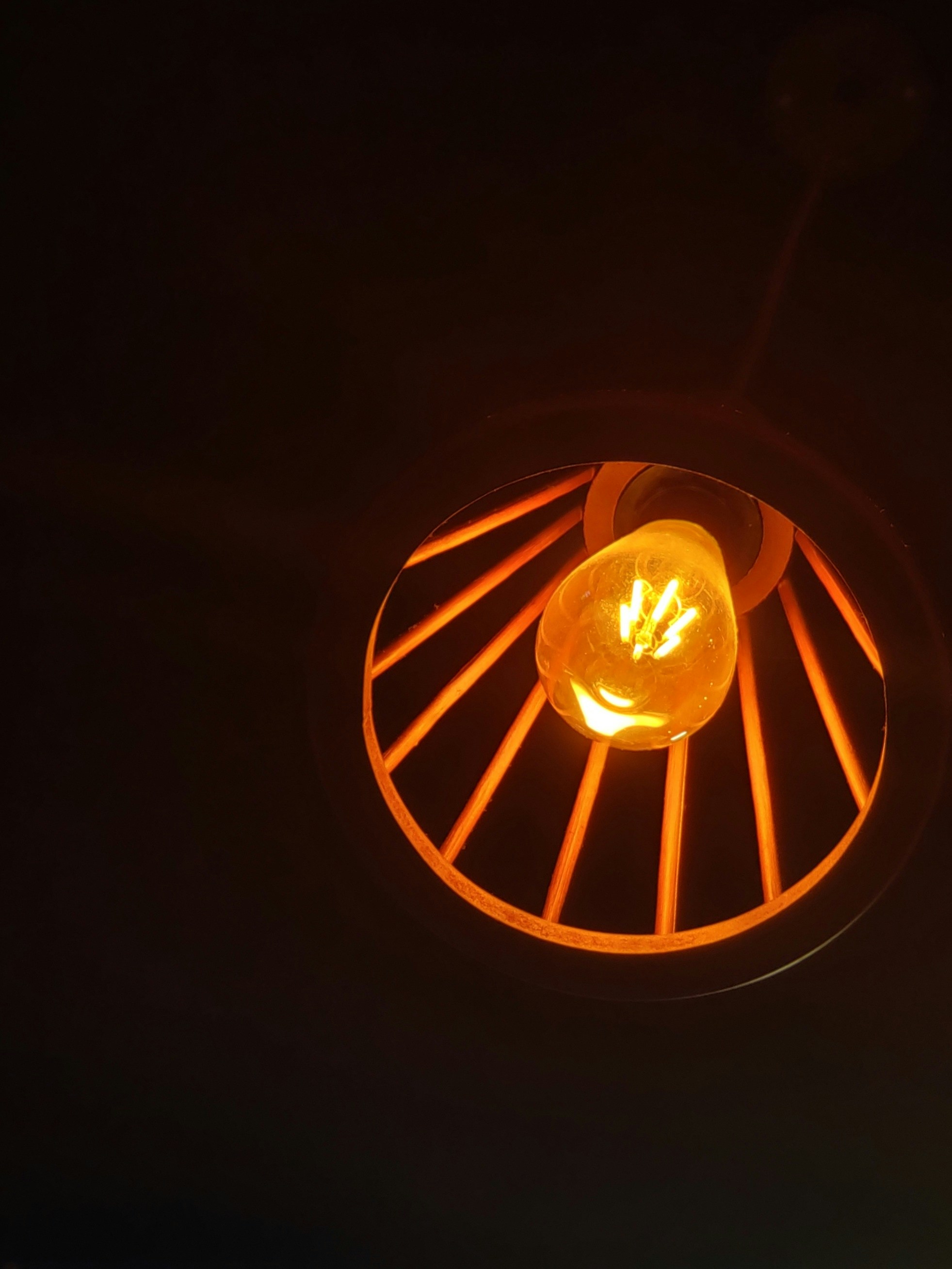 A vintage light bulb radiates a warm orange glow, framed by a circular grill against a dark backdrop.