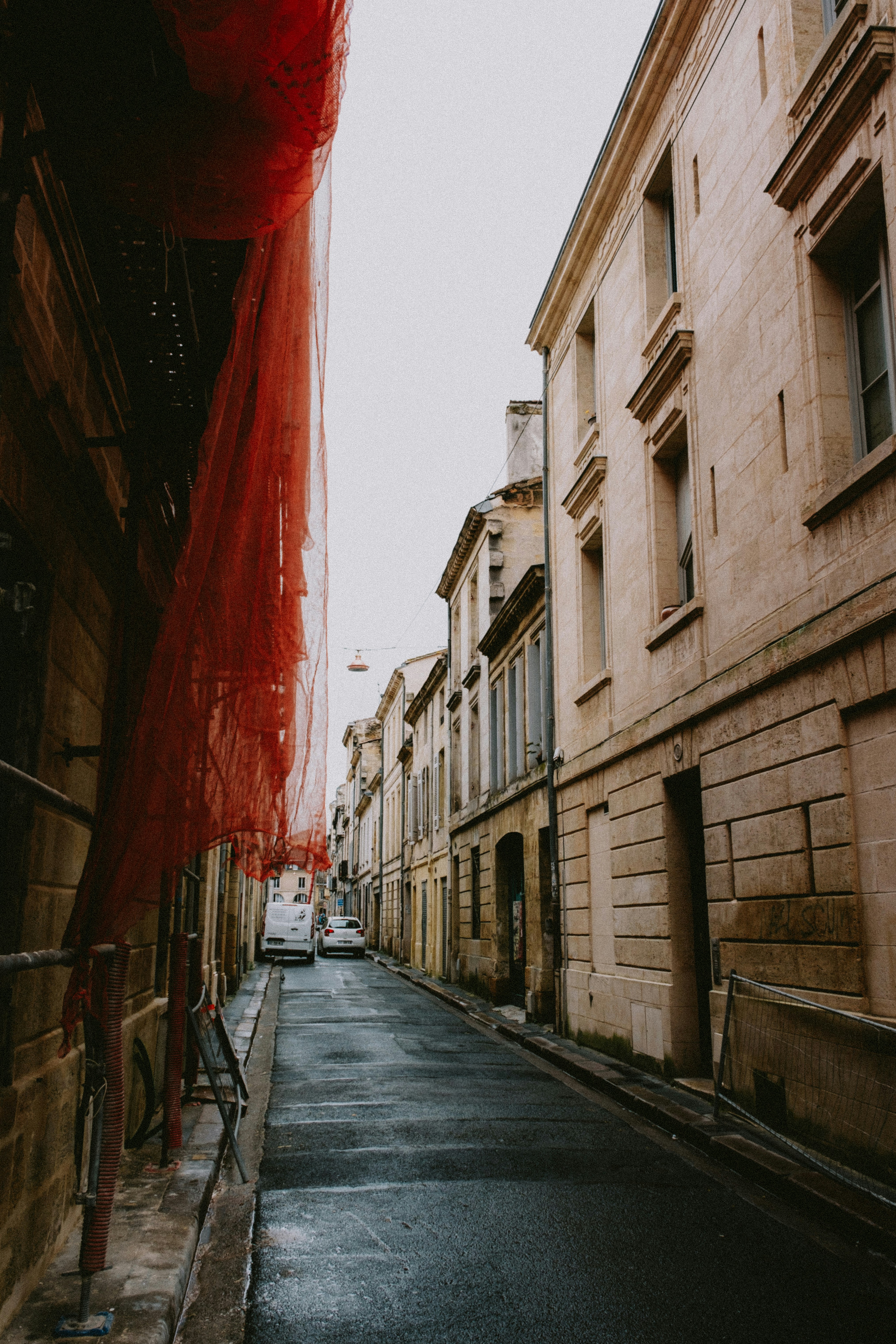 Narrow European street flanked by historic stone buildings with red netting overhead.