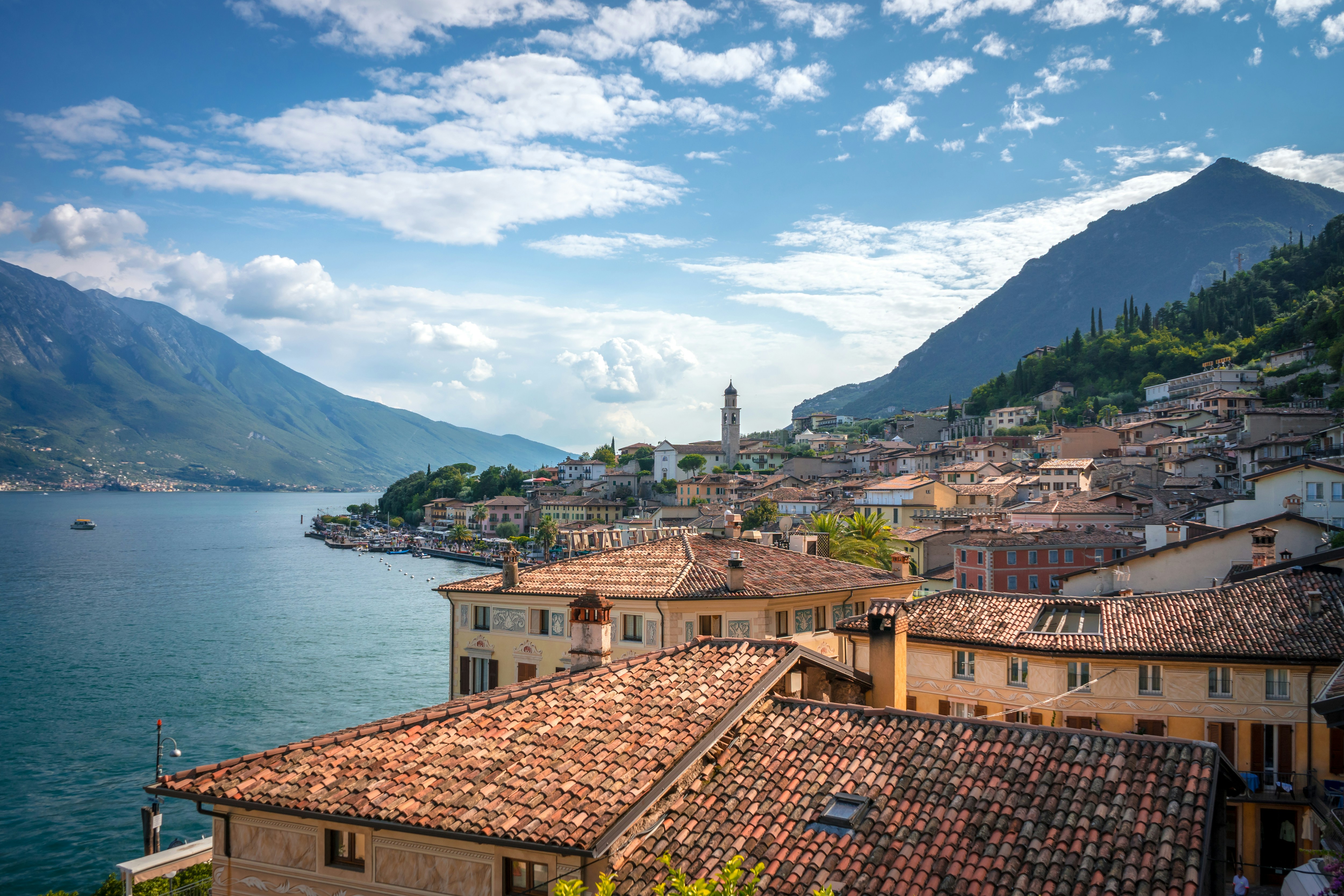 Charming hillside town with terracotta rooftops overlooking a tranquil lake under a bright blue sky.