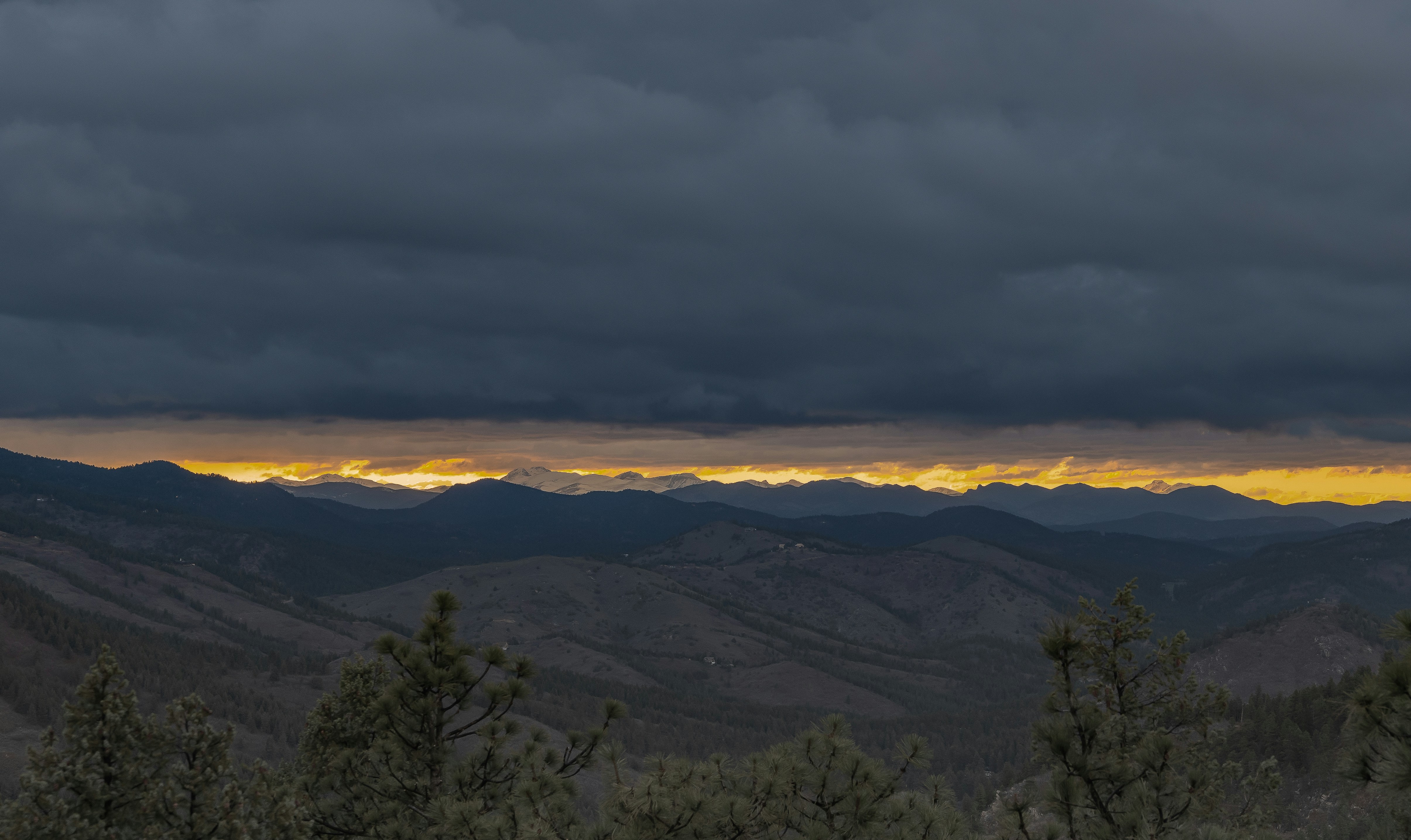 Golden light peeks through dark clouds over rolling mountain ridges, creating a dramatic contrast in the twilight sky.