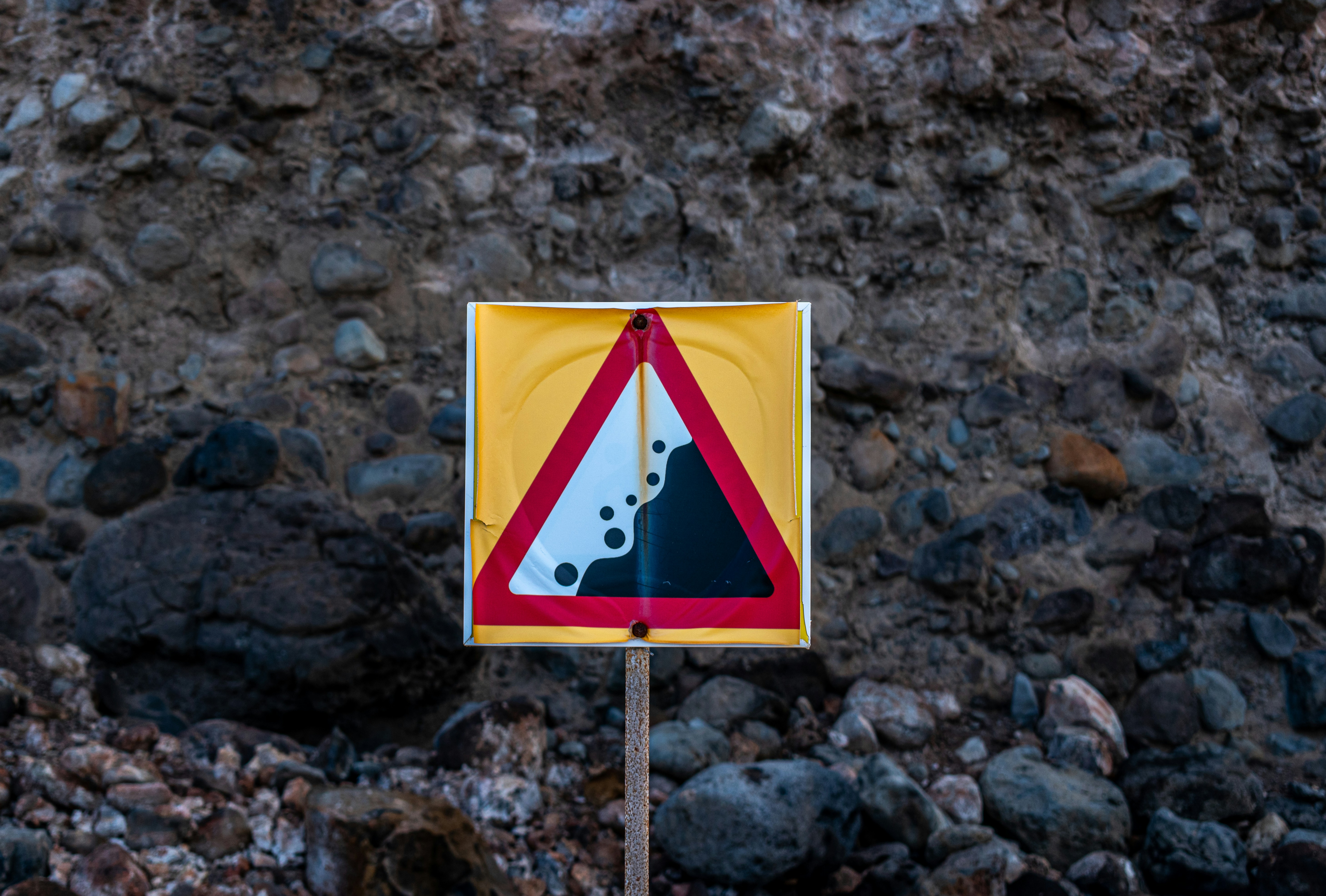 A yellow and red sign sitting on top of a rocky hillside photo – Free ...