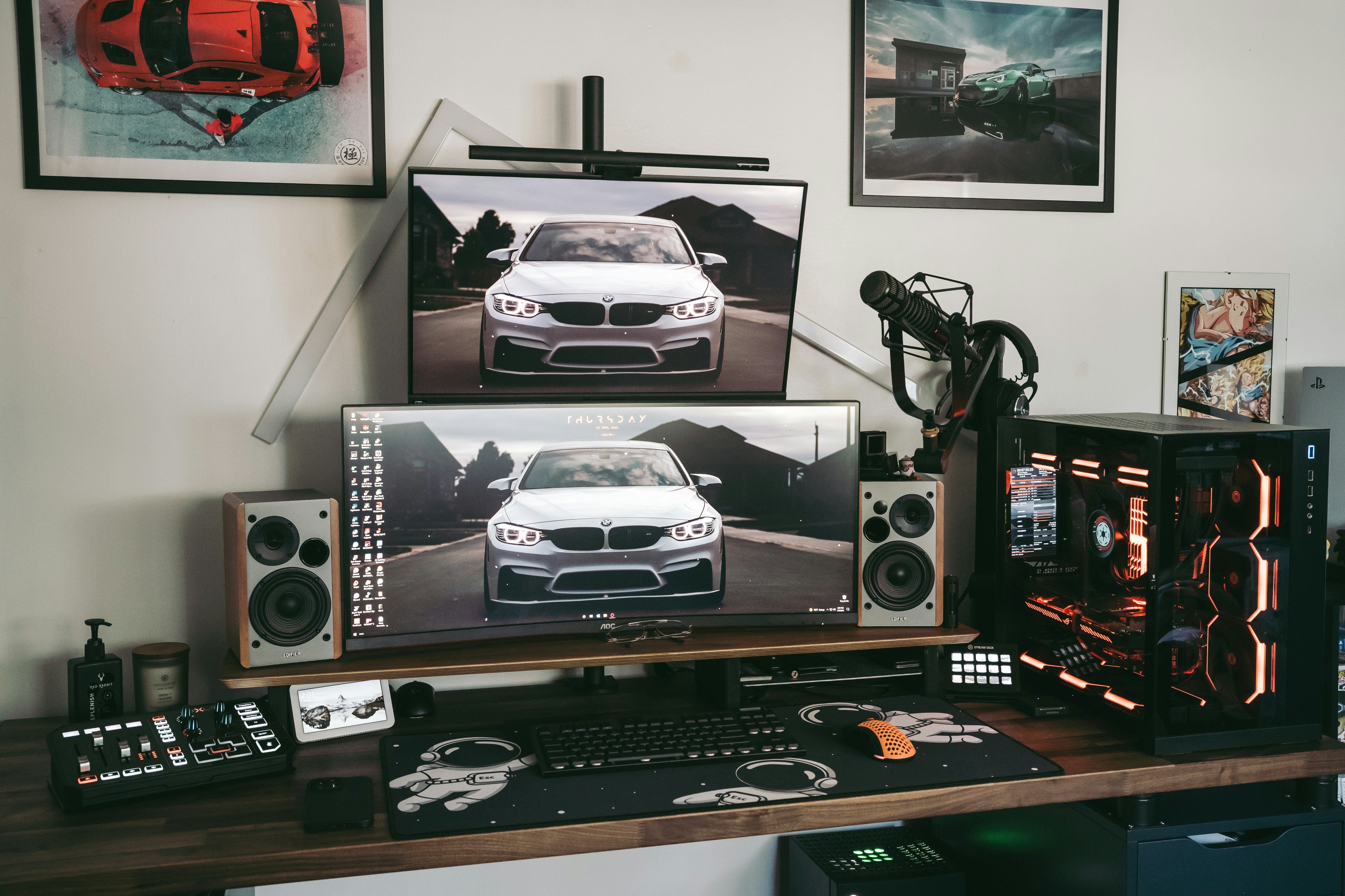 A modern workspace featuring dual monitors displaying a BMW, high-quality speakers, and a sleek gaming PC setup against a backdrop of automotive art.