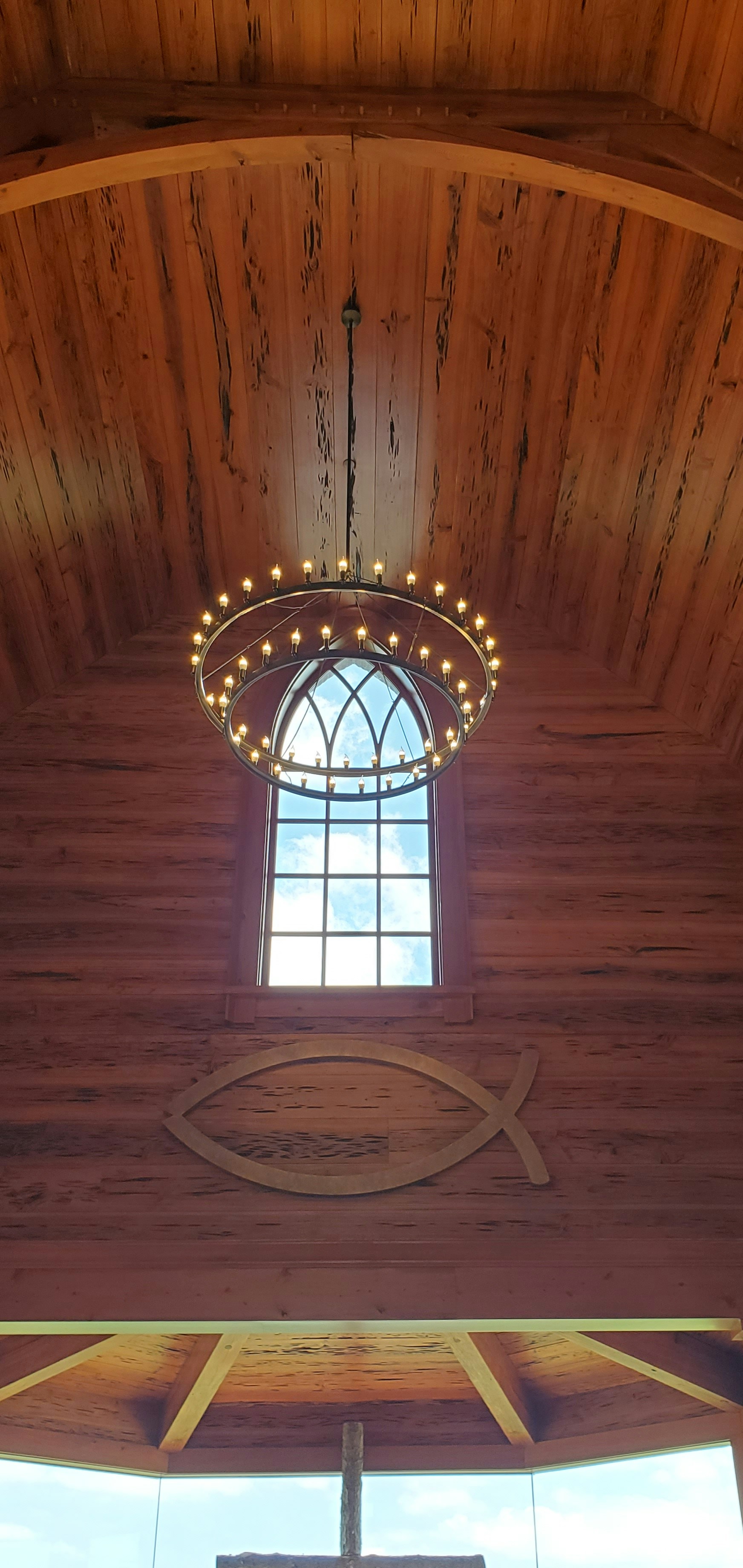 Cedar-Chapel Halo: Circular Chandelier Framing a Window and Ichthys Symbol