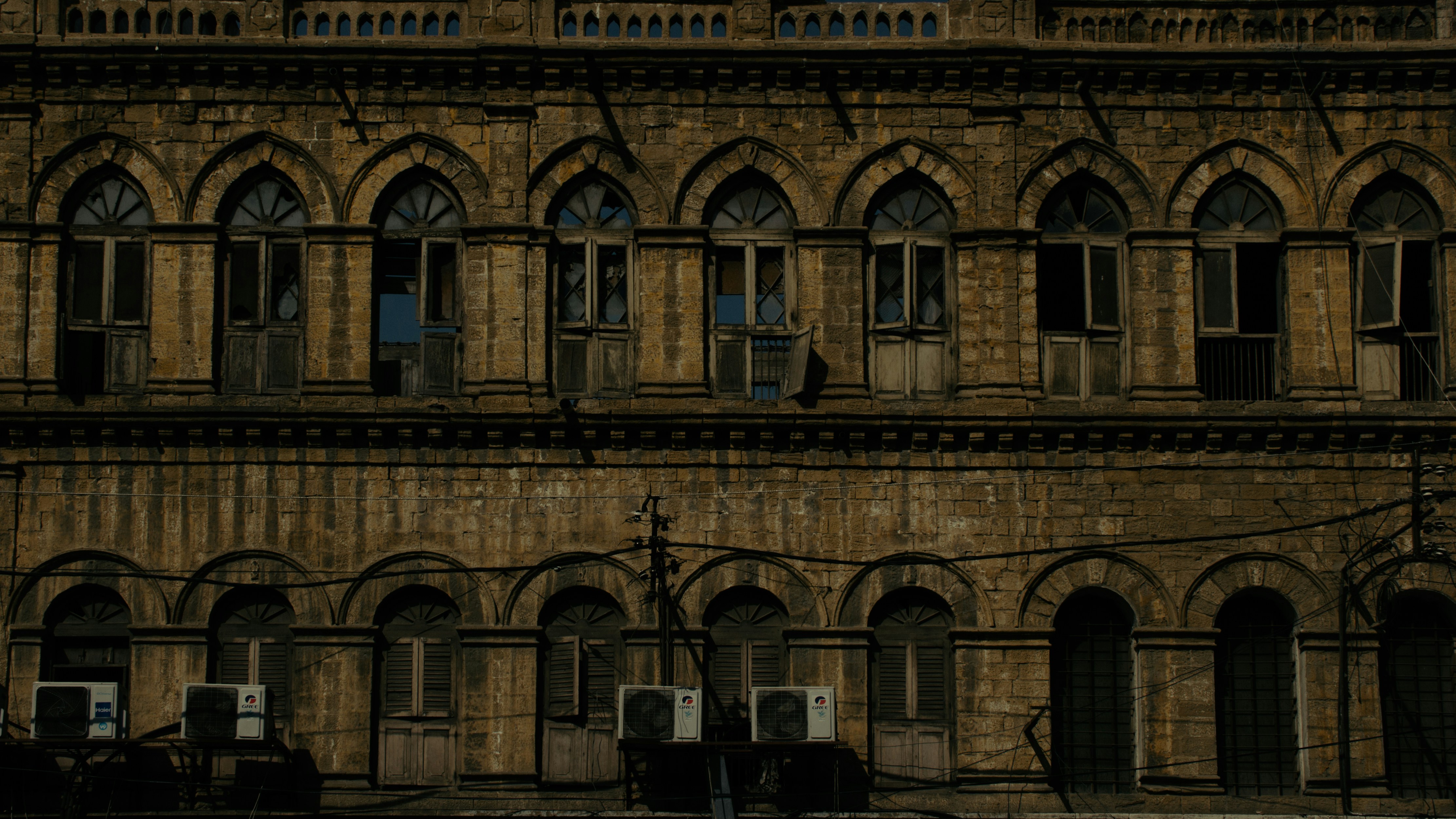 Historic stone building in Karachi with arched windows and weathered wooden shutters.