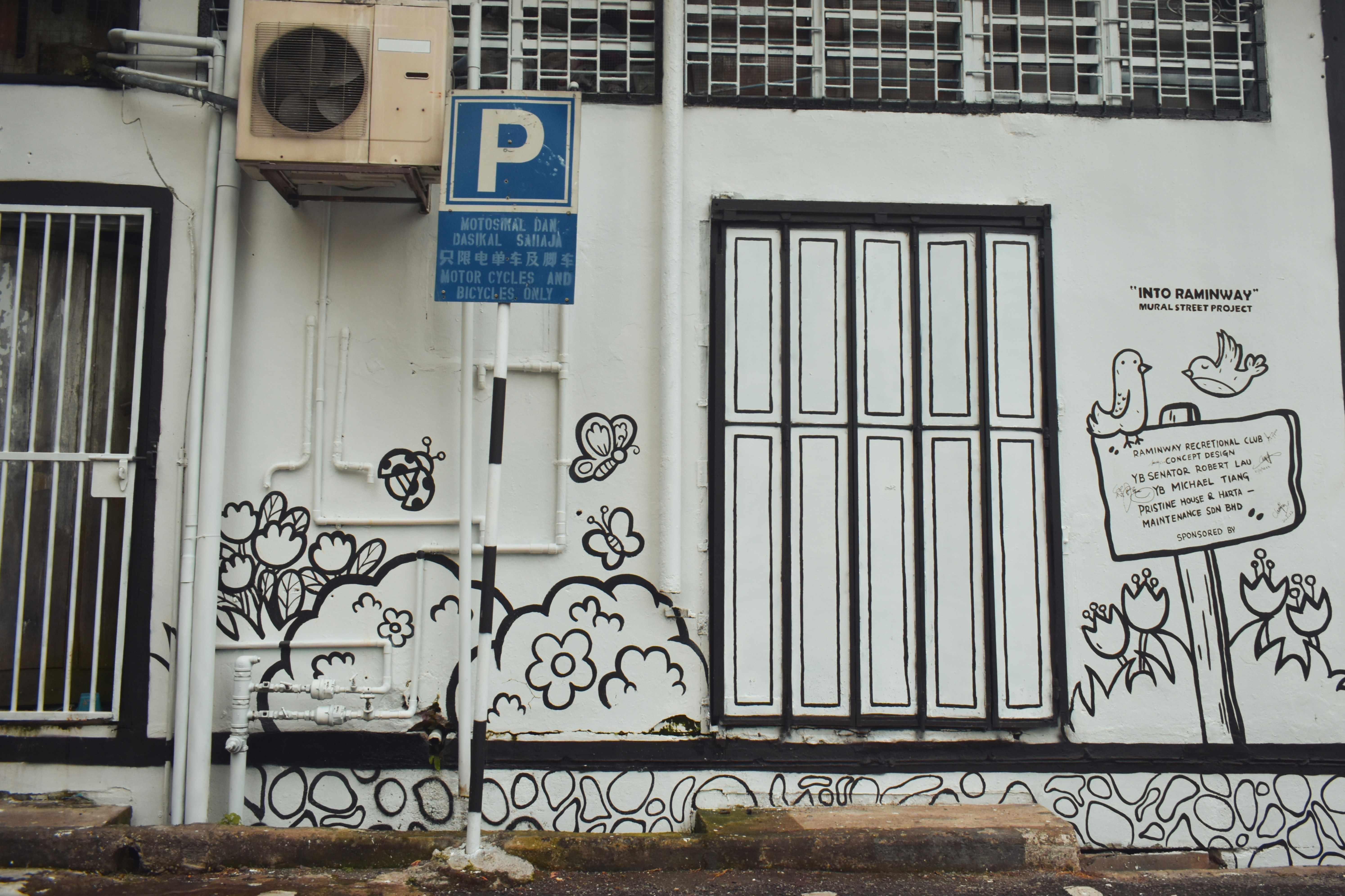 Street art featuring floral designs on a white wall beside a parking sign and an air conditioning unit.