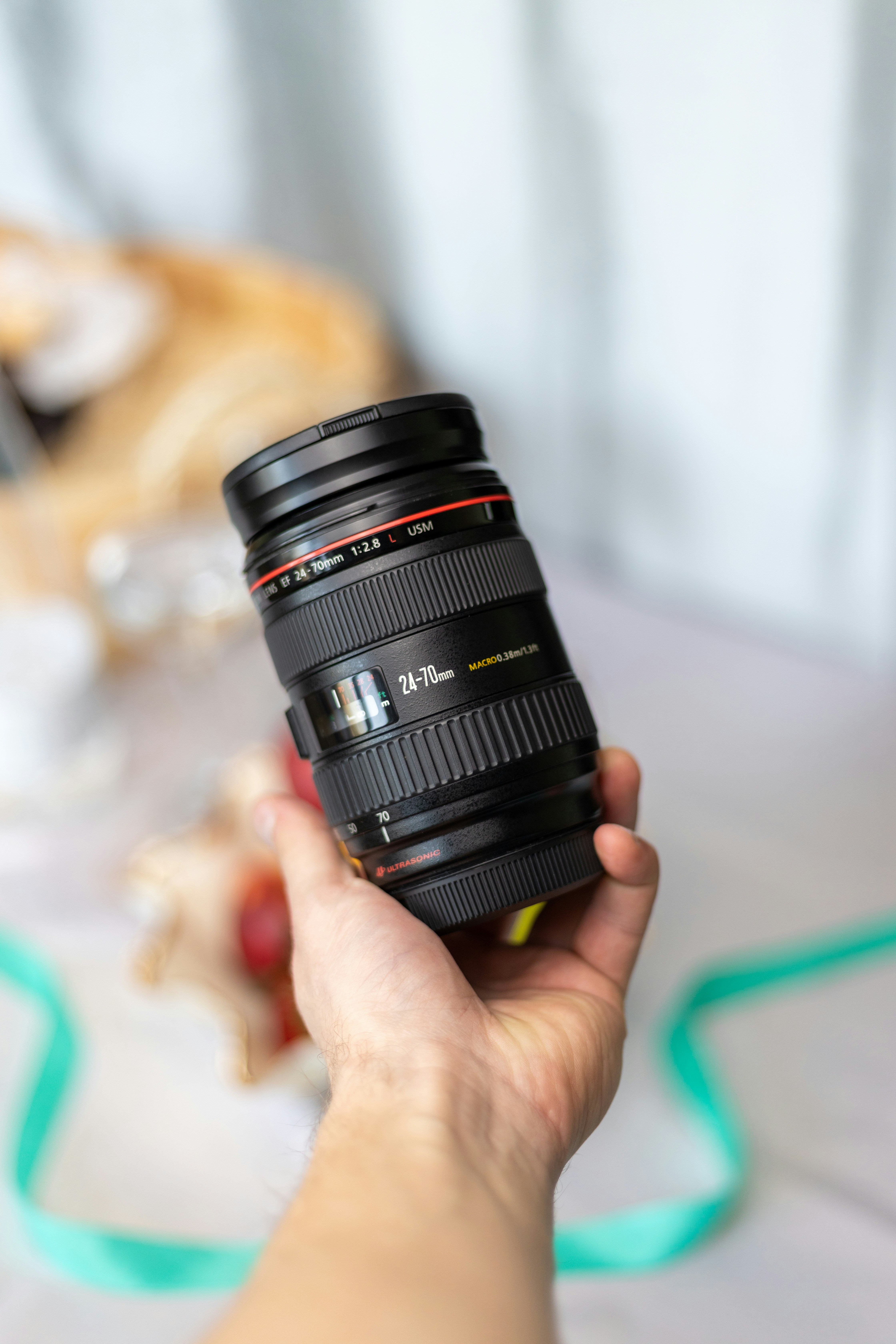 A Canon 24-70mm lens held in hand against a softly blurred background, showcasing its design and craftsmanship.