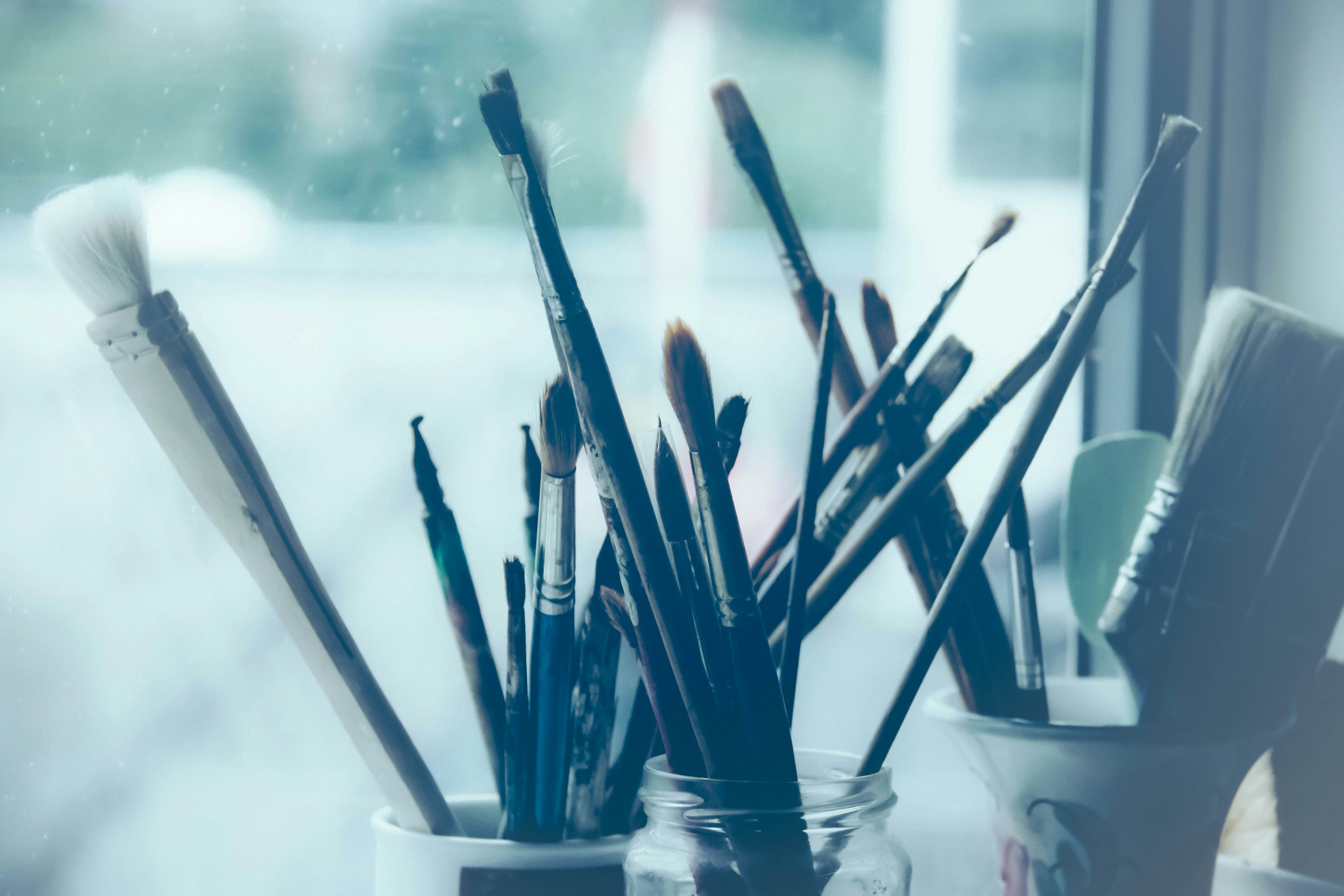 Paint brushes in glass jars near a softly lit window, suggesting creativity and inspiration.