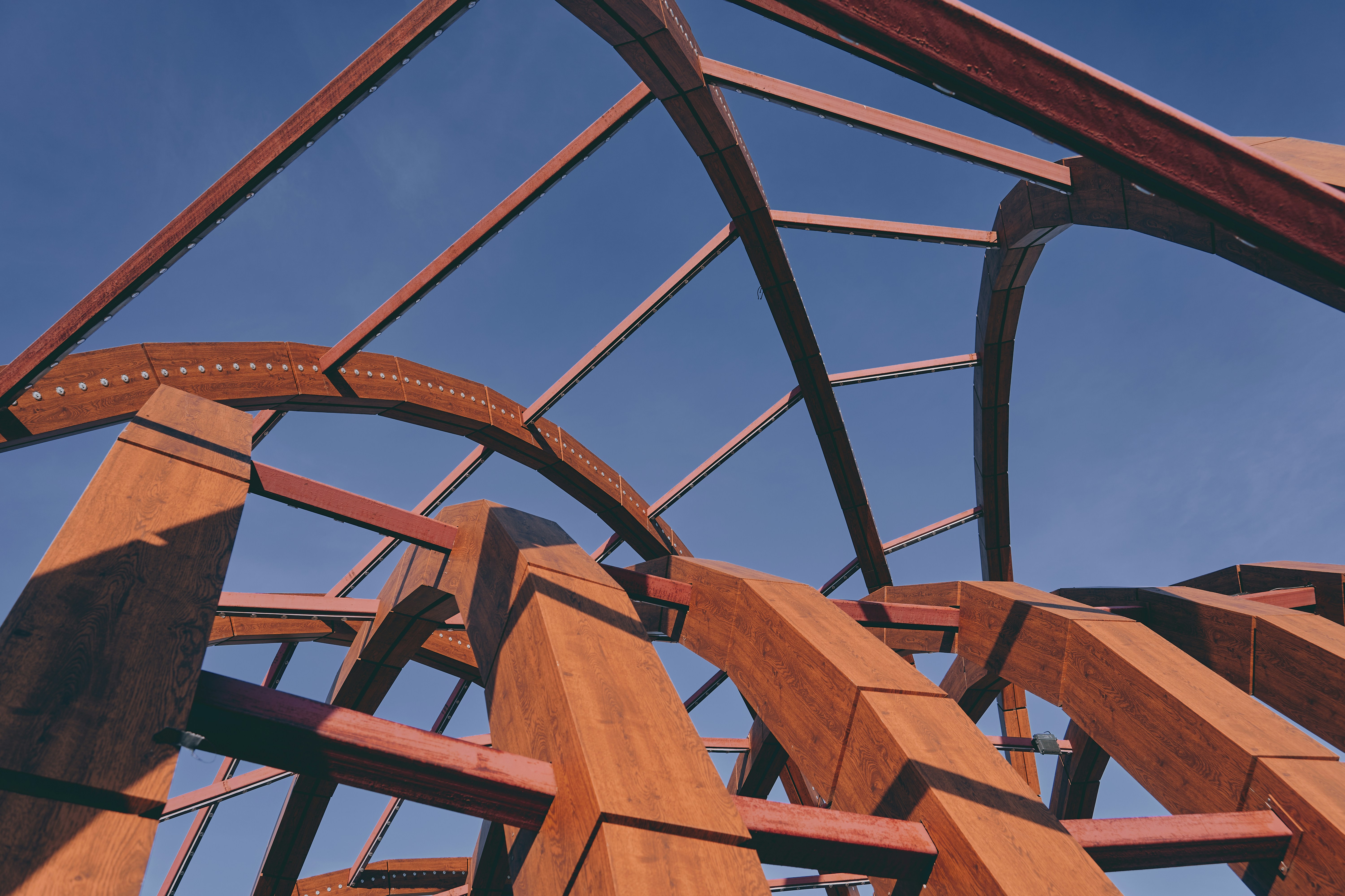 Intricate wooden framework of a structure under a clear blue sky, showcasing modern architectural design elements.