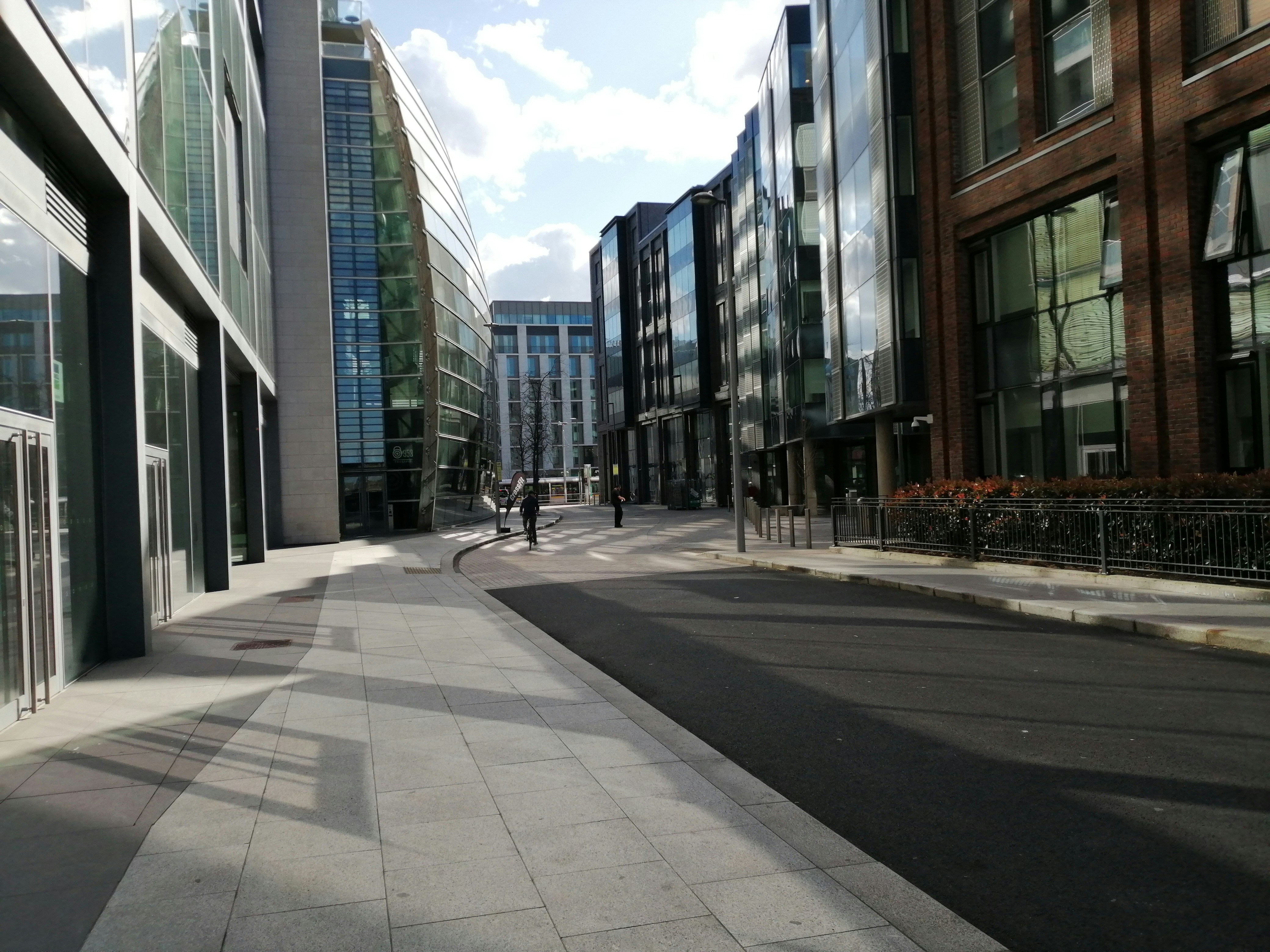 Modern glass and brick buildings line an empty city street under a partly cloudy sky.