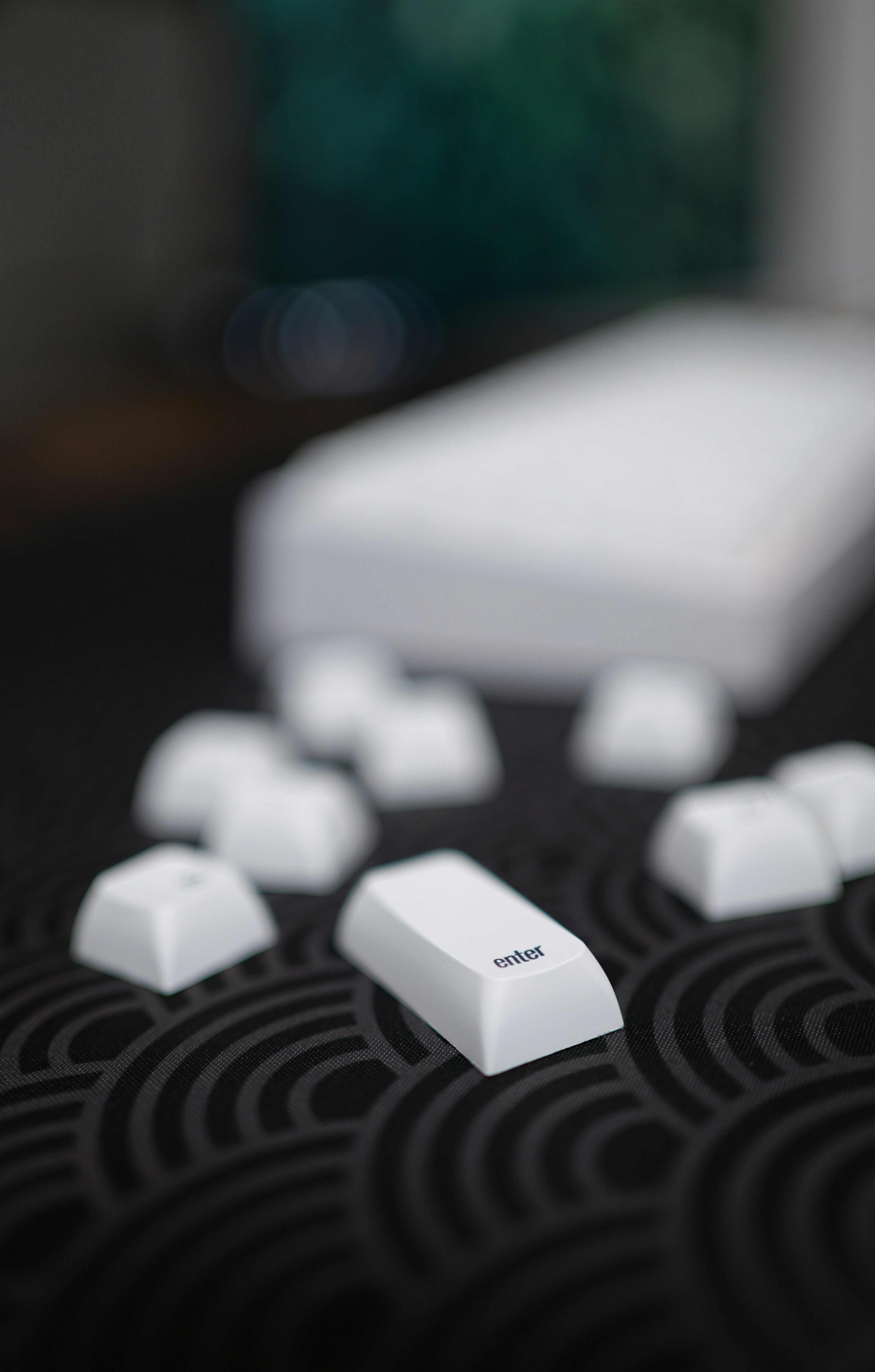 Close-up of white keyboard keys on a textured black surface, highlighting the 'enter' key among scattered keys. 
