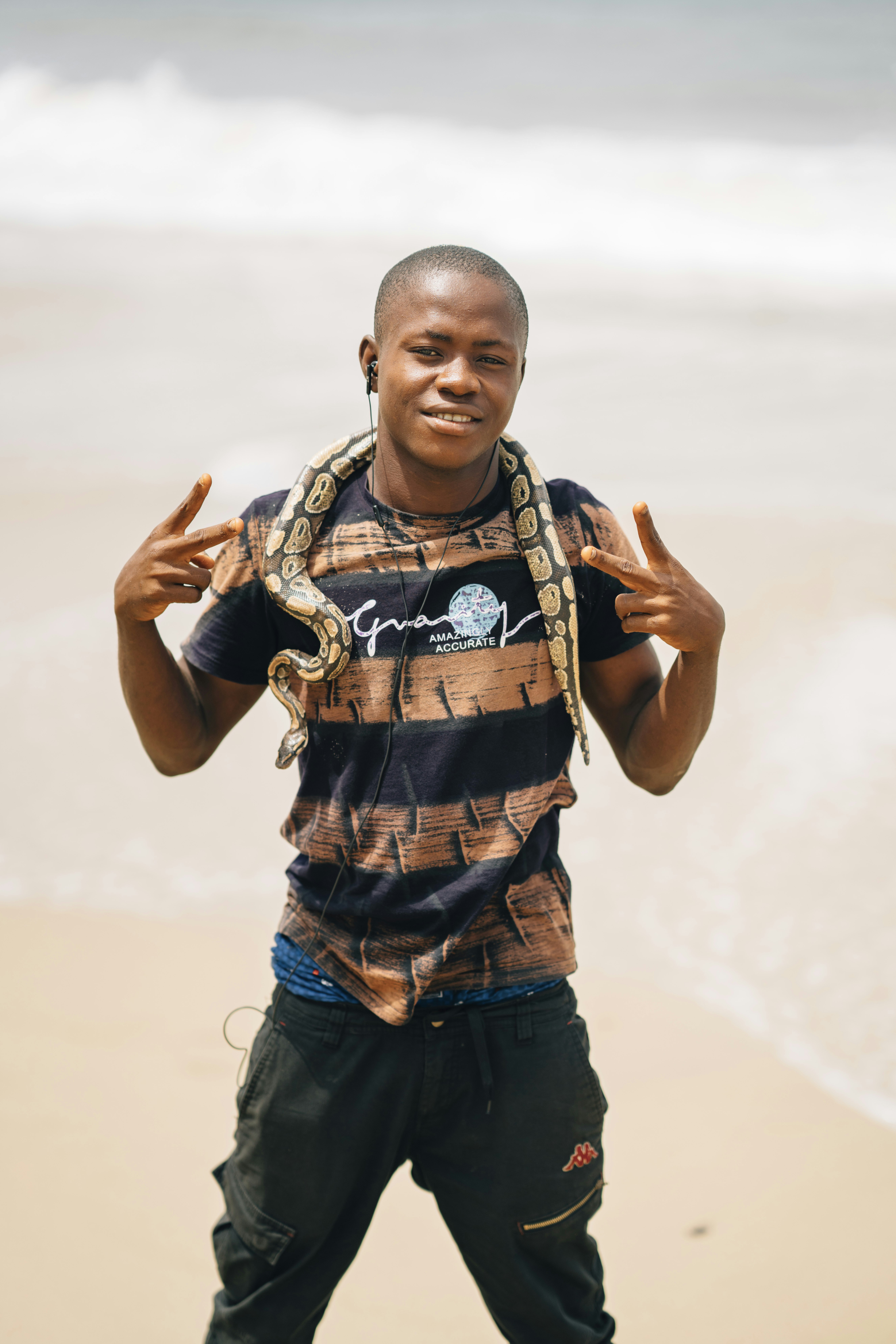 Young man posing confidently on the beach with a snake draped around his neck, showcasing a unique bond with nature.