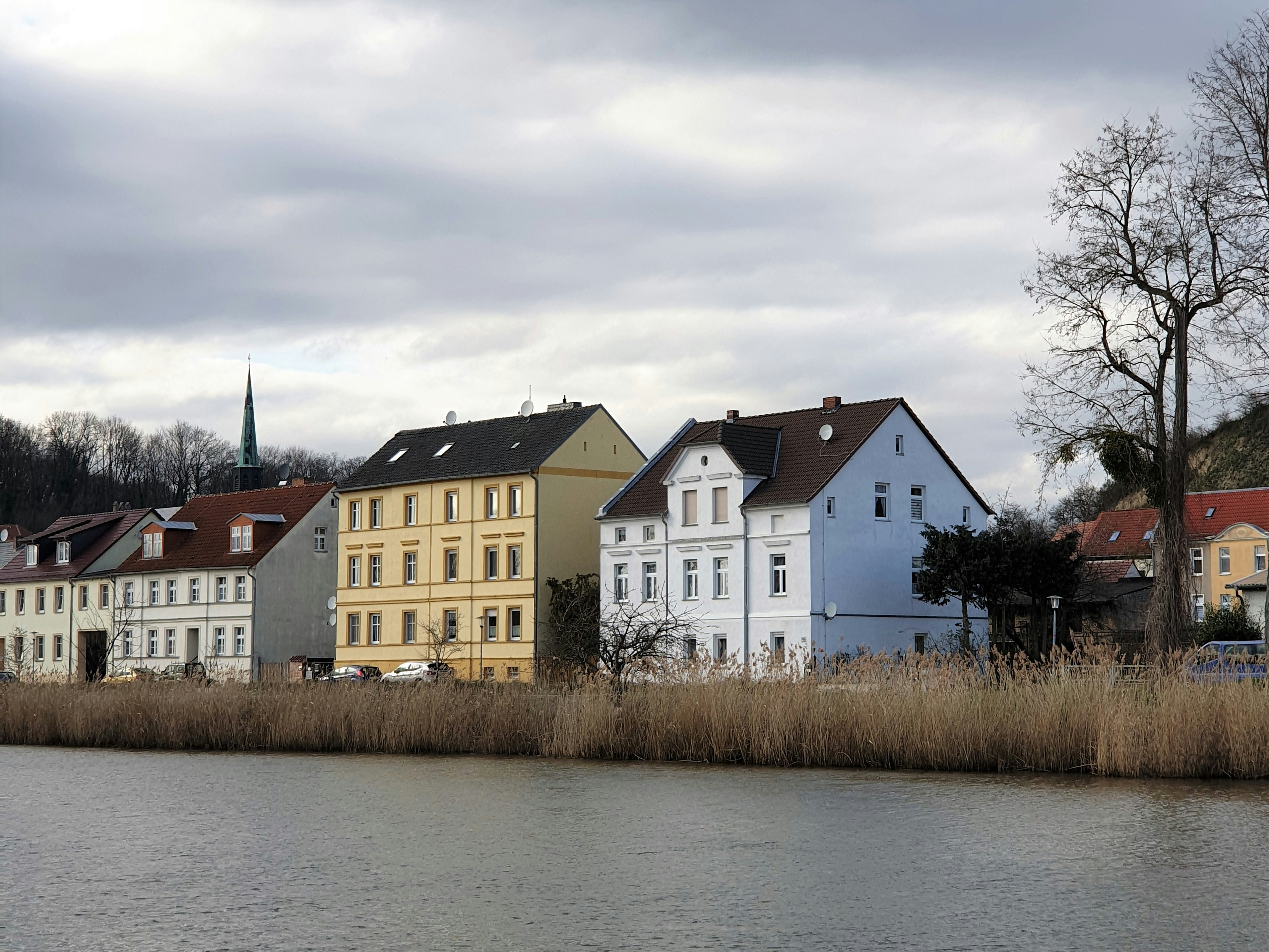 Pastel Row by the River: Quiet European Village Under Cloudy Skies