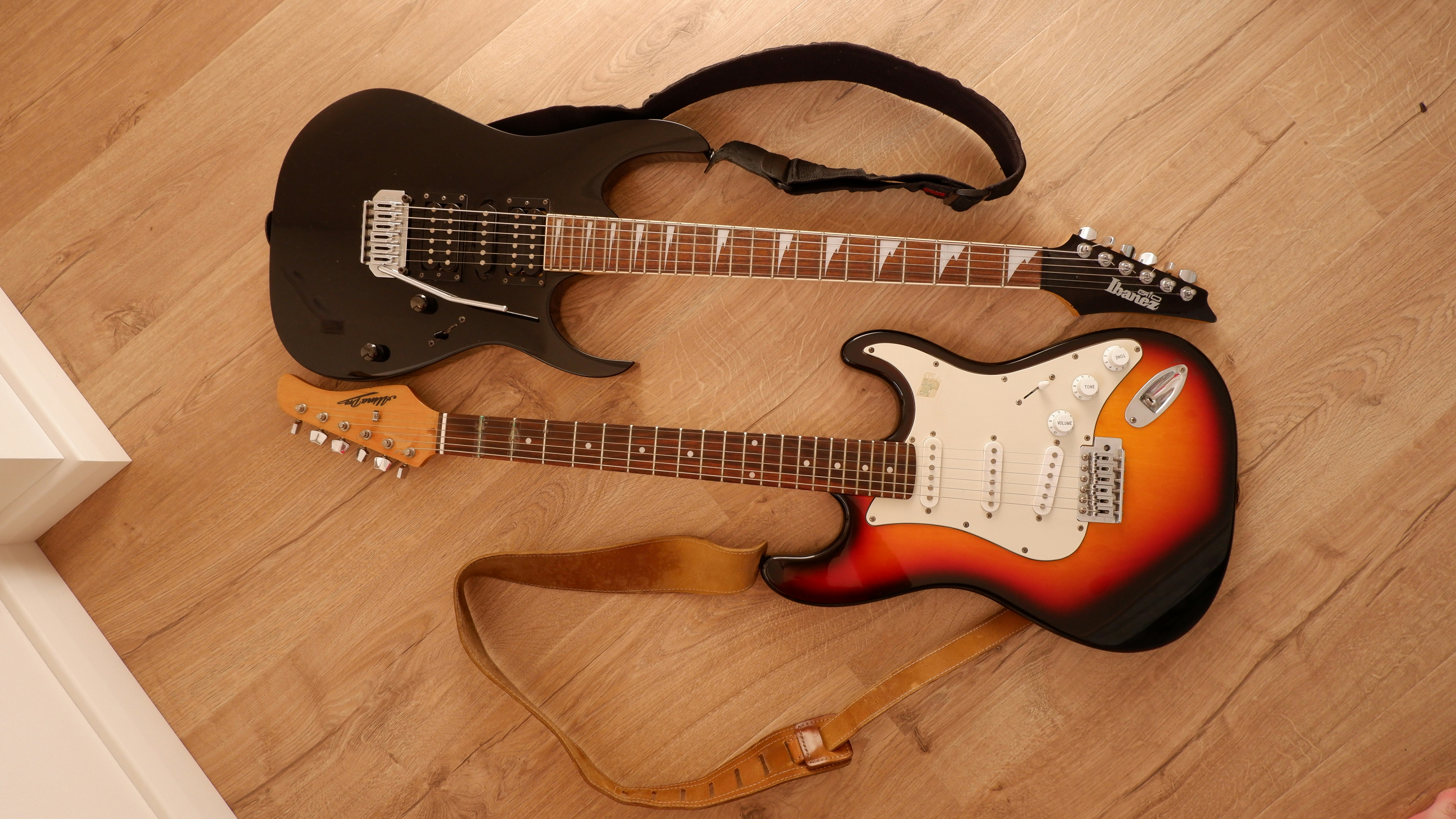 Two electric guitars laid on a wooden floor, showcasing their distinct designs and colors. The black guitar features a sleek body, while the sunburst model has a classic appeal.