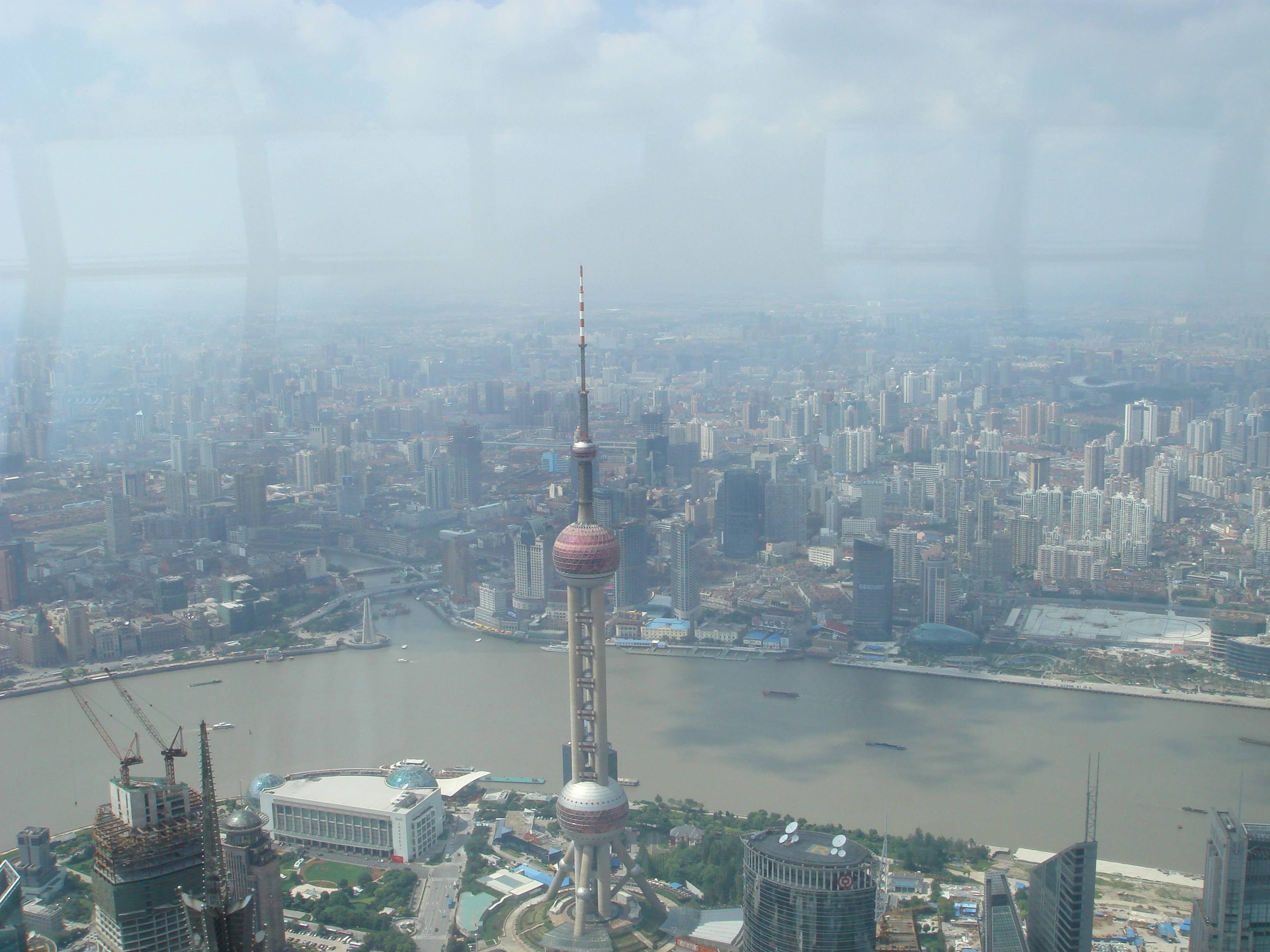 Aerial view of Shanghai showcasing the Oriental Pearl Tower amidst a sprawling cityscape and the Huangpu River below.