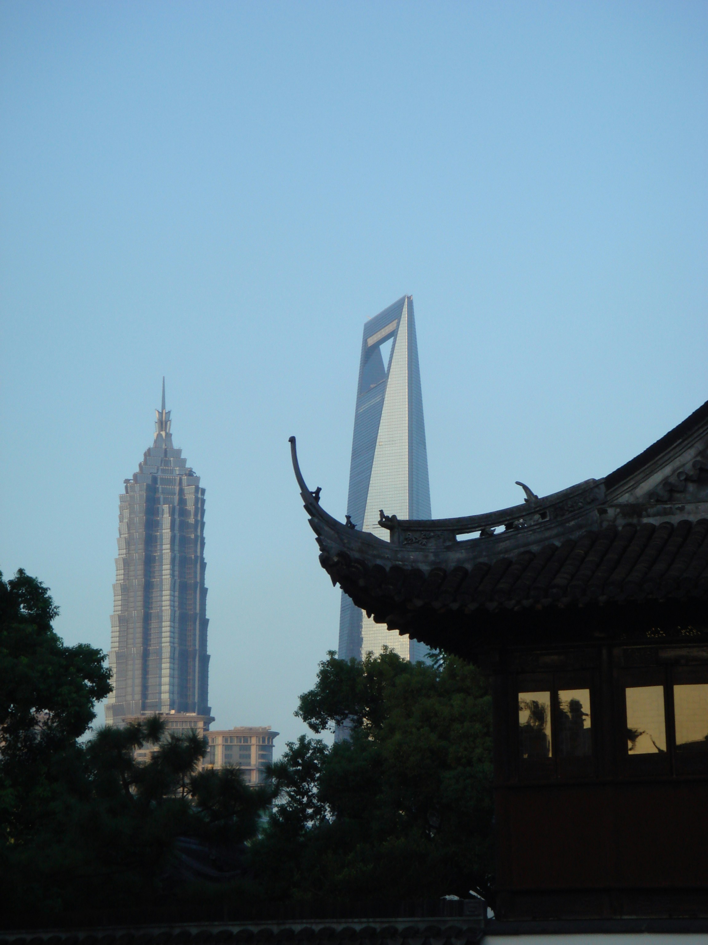 Photograph of traditional curved-roof architecture in the foreground with Shanghai's modern skyline behind, featuring Jin Mao Tower and the Shanghai World Financial Center, under a clear blue sky.