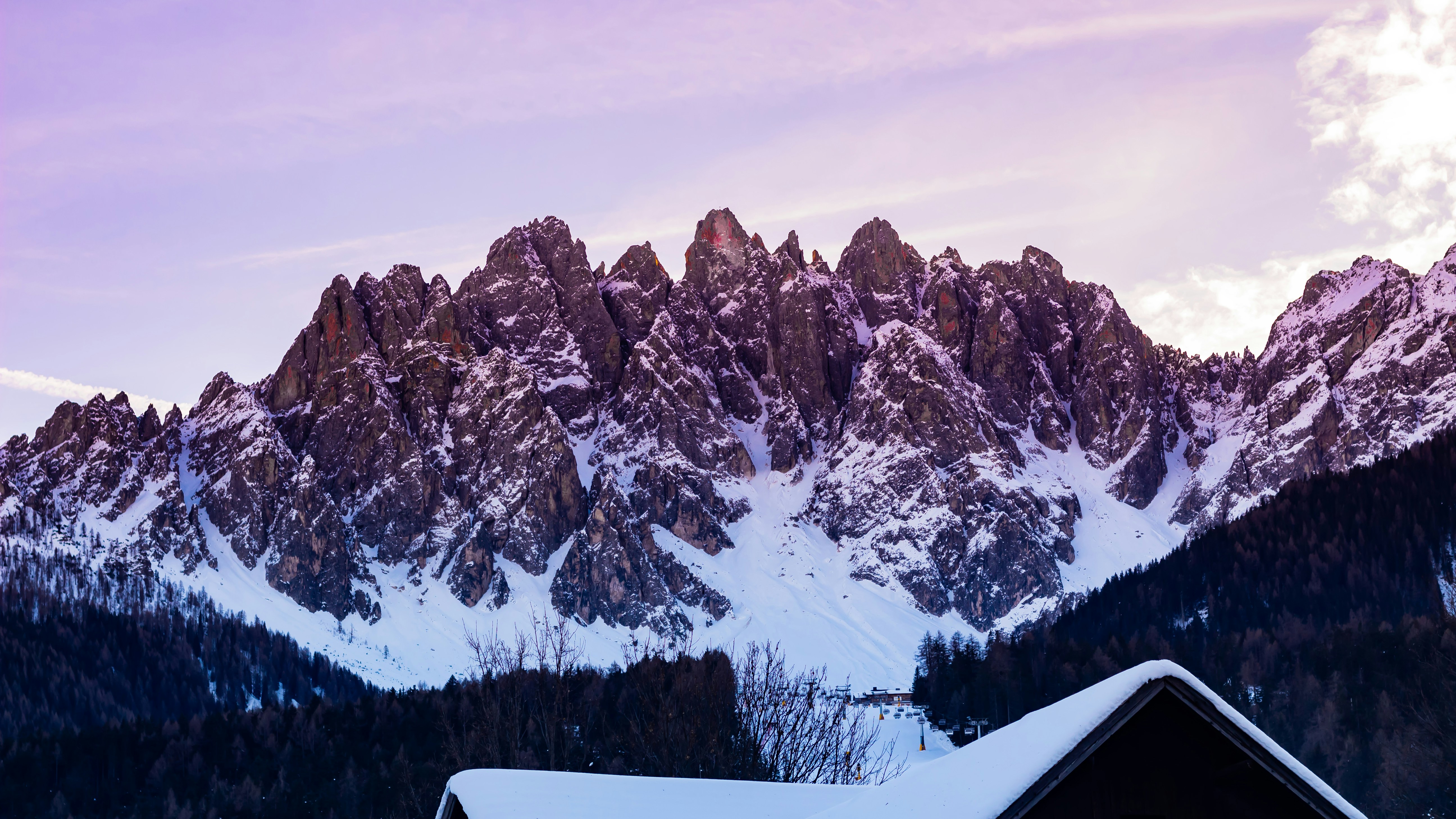 Snow-capped mountain range under a purple-tinged sky, with a silhouetted roof in the foreground.
