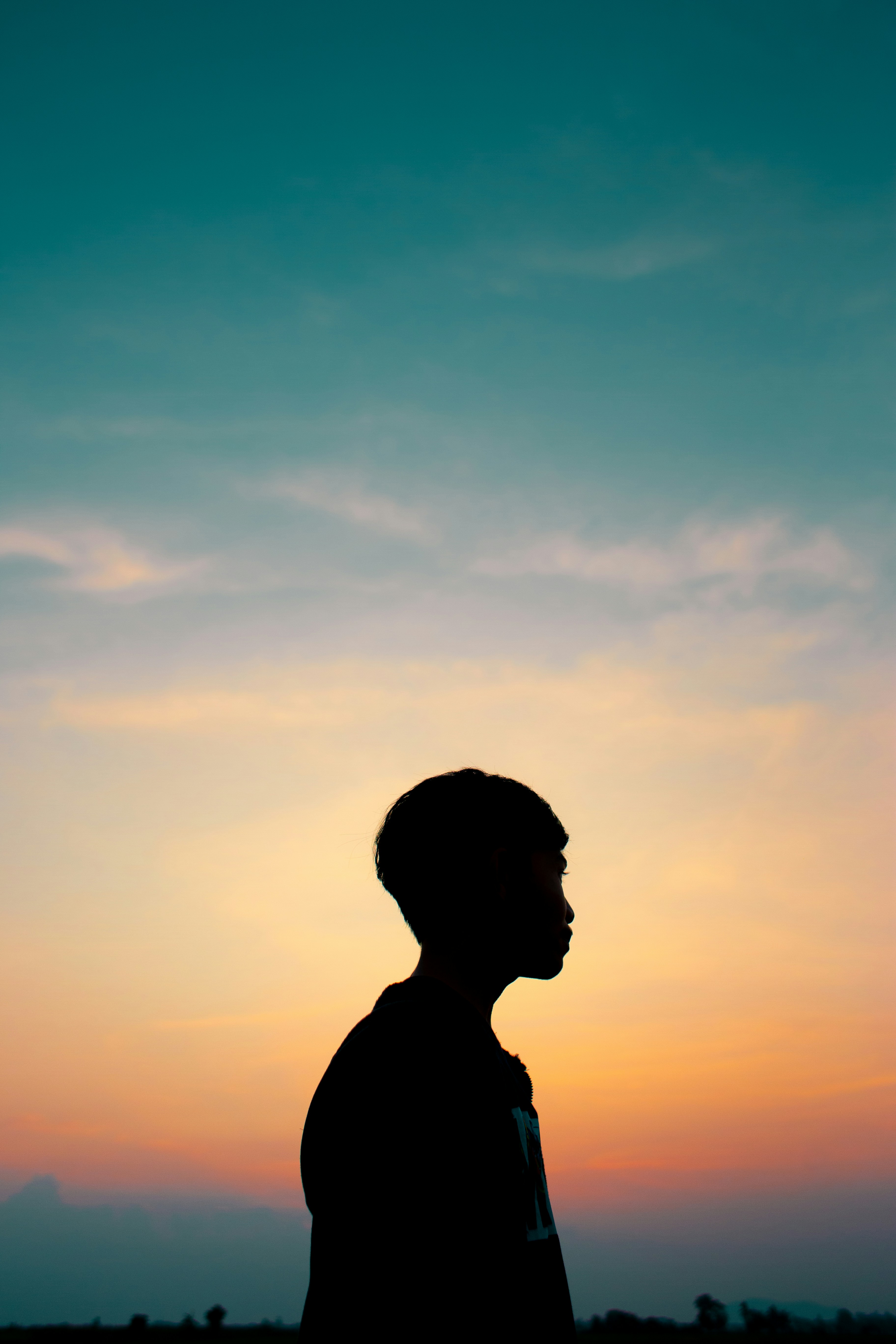 Silhouette of a person with a serene expression, framed by a vibrant sunset sky transitioning from blue to orange.