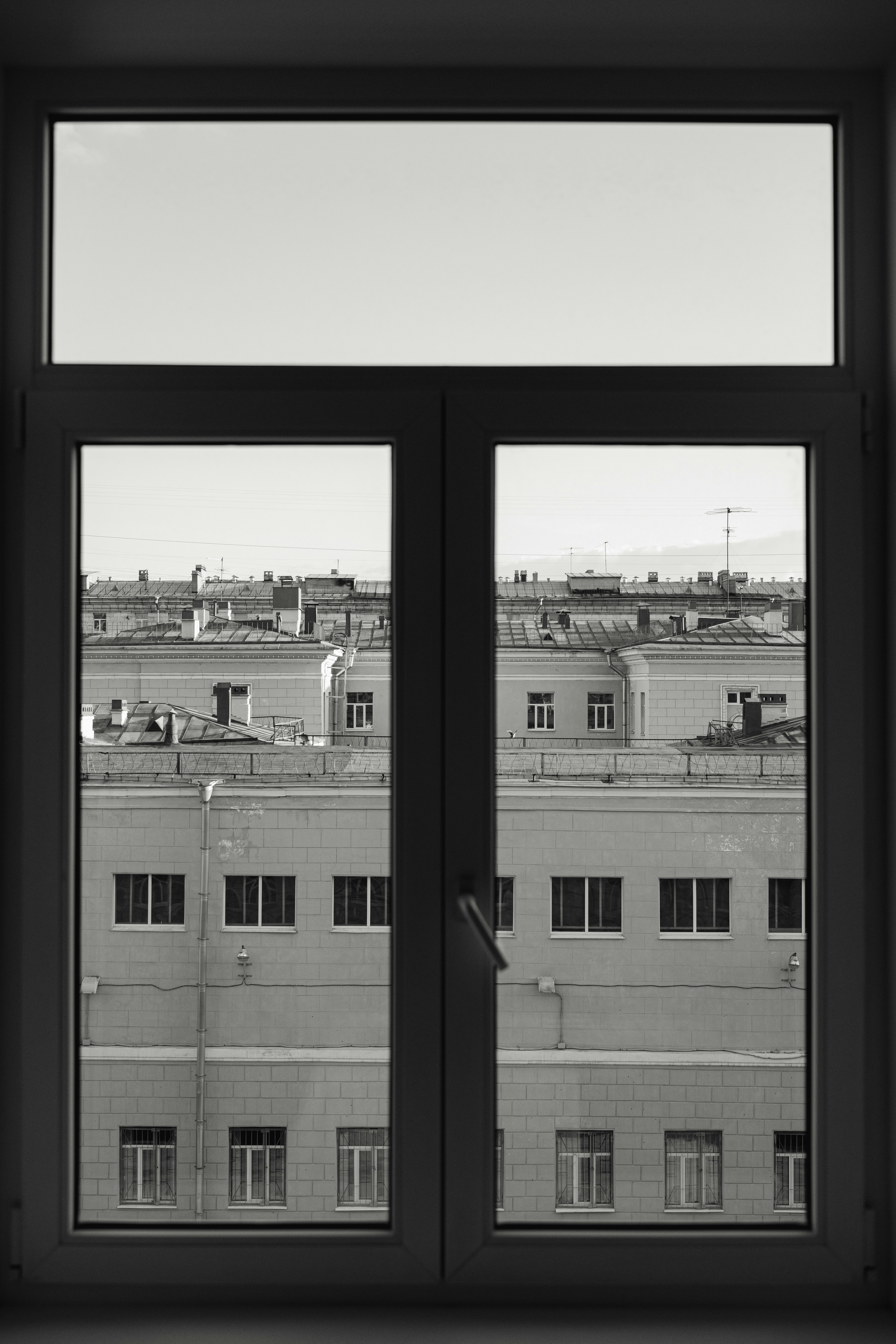 View of city rooftops framed by a window, showcasing architectural lines and textures in monochrome.