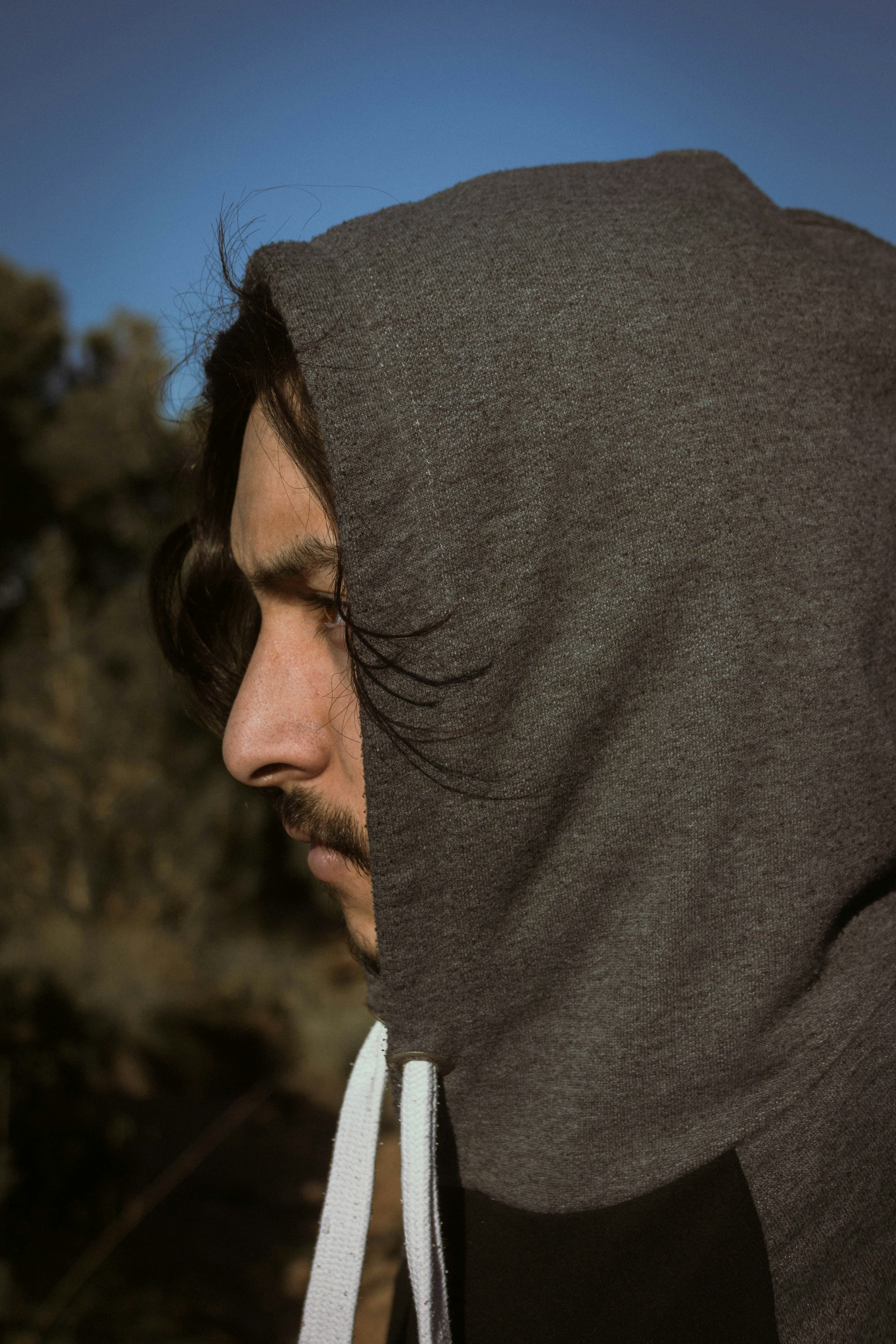 Profile in Gray: Sunlit Hoodie Portrait Against a Clear Sky