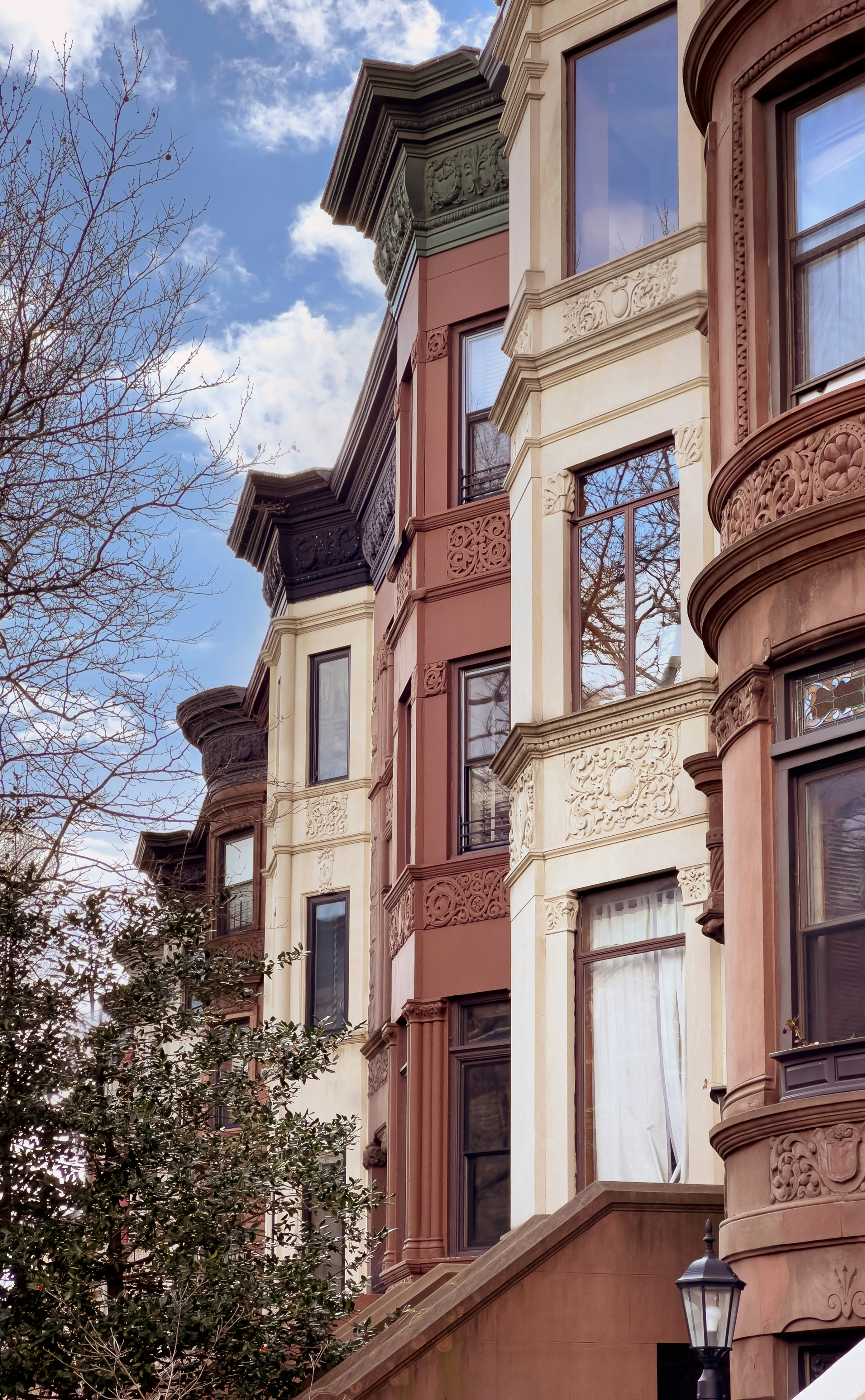 Row of ornate brownstone buildings showcasing intricate architectural details under a cloudy sky.