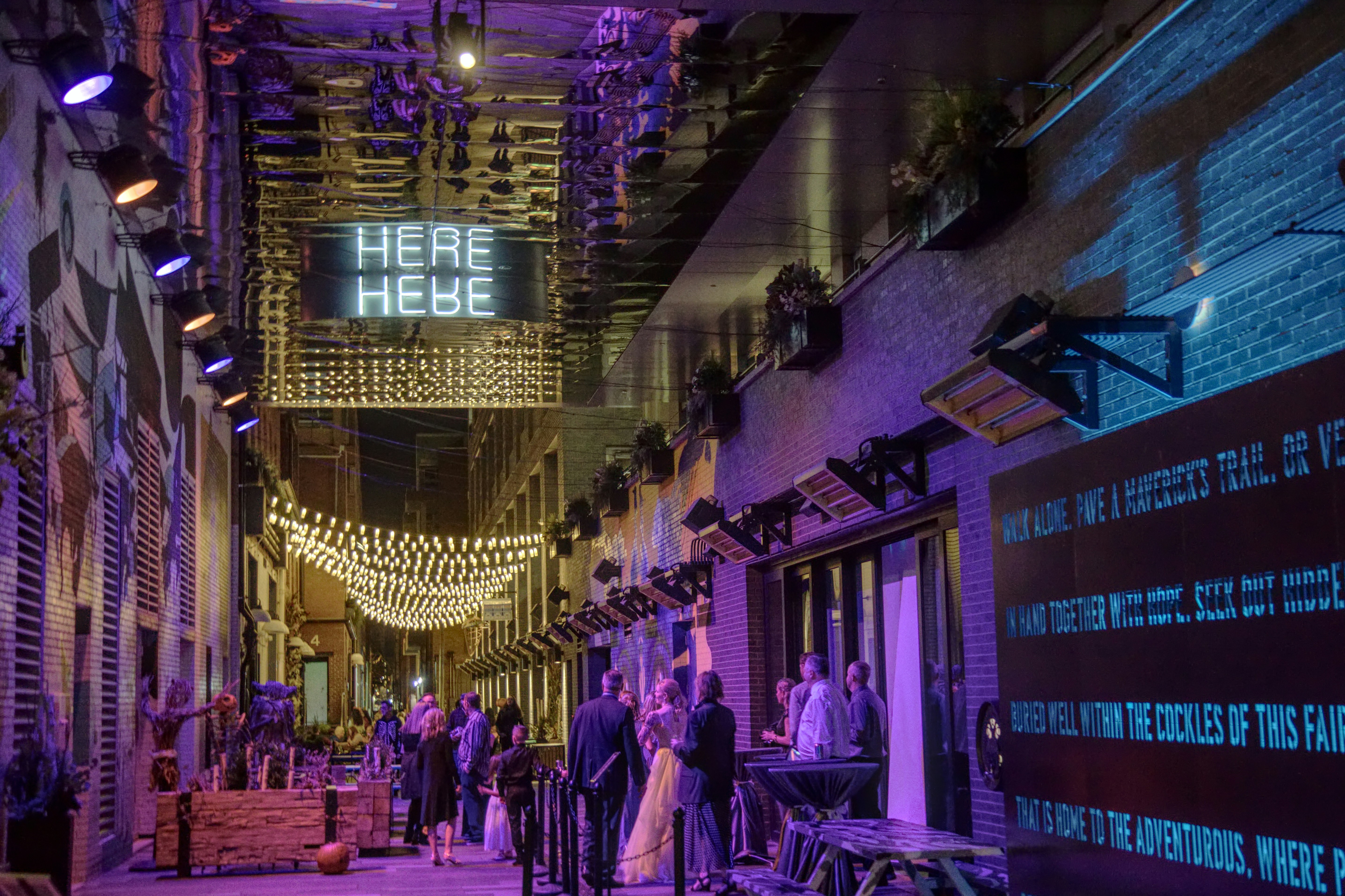 Neon Canopy Over a Night Alley: People Beneath Indigo Light
