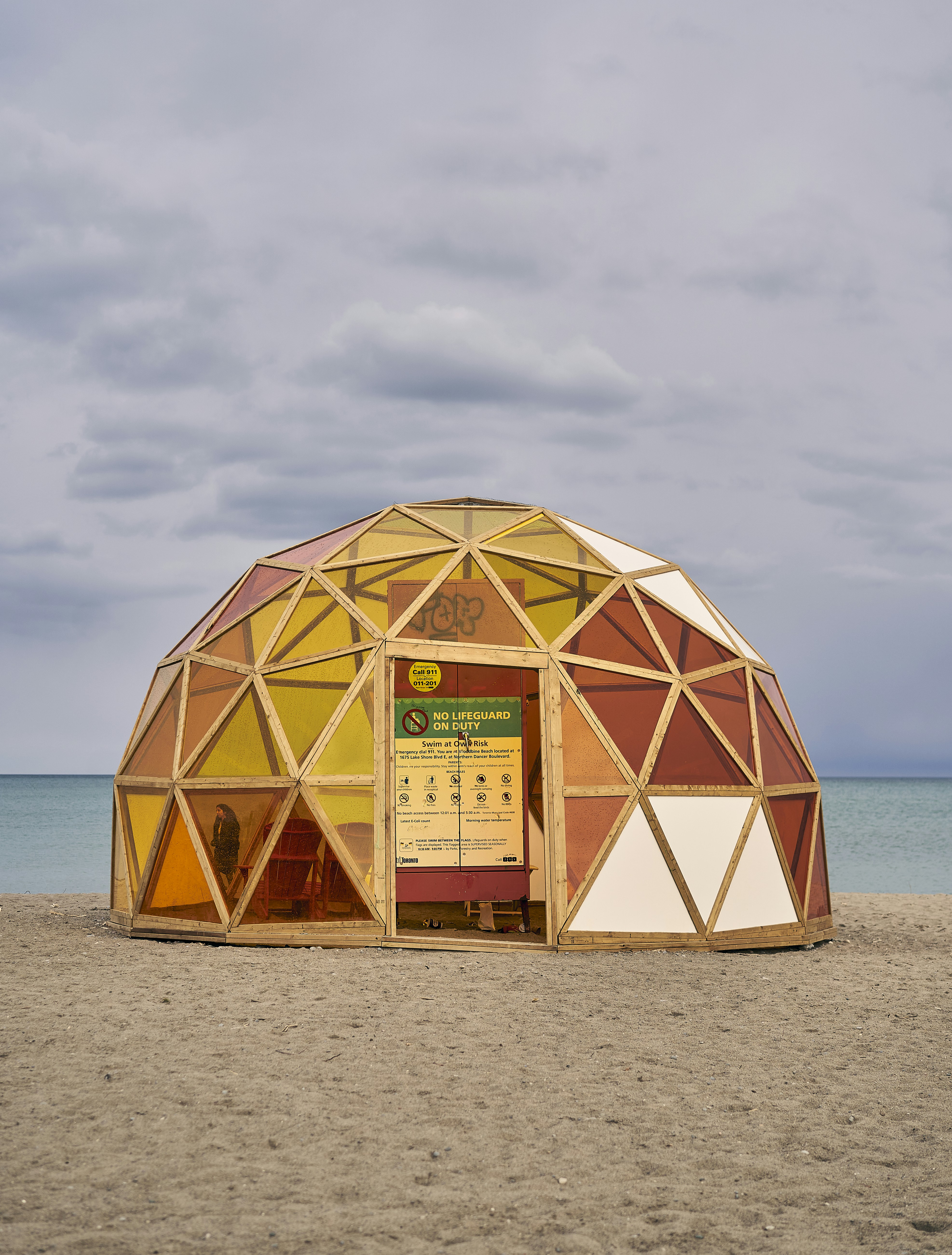 Colorful dome structure on sandy beach, featuring a sign with safety information. The tranquil ocean serves as a backdrop.