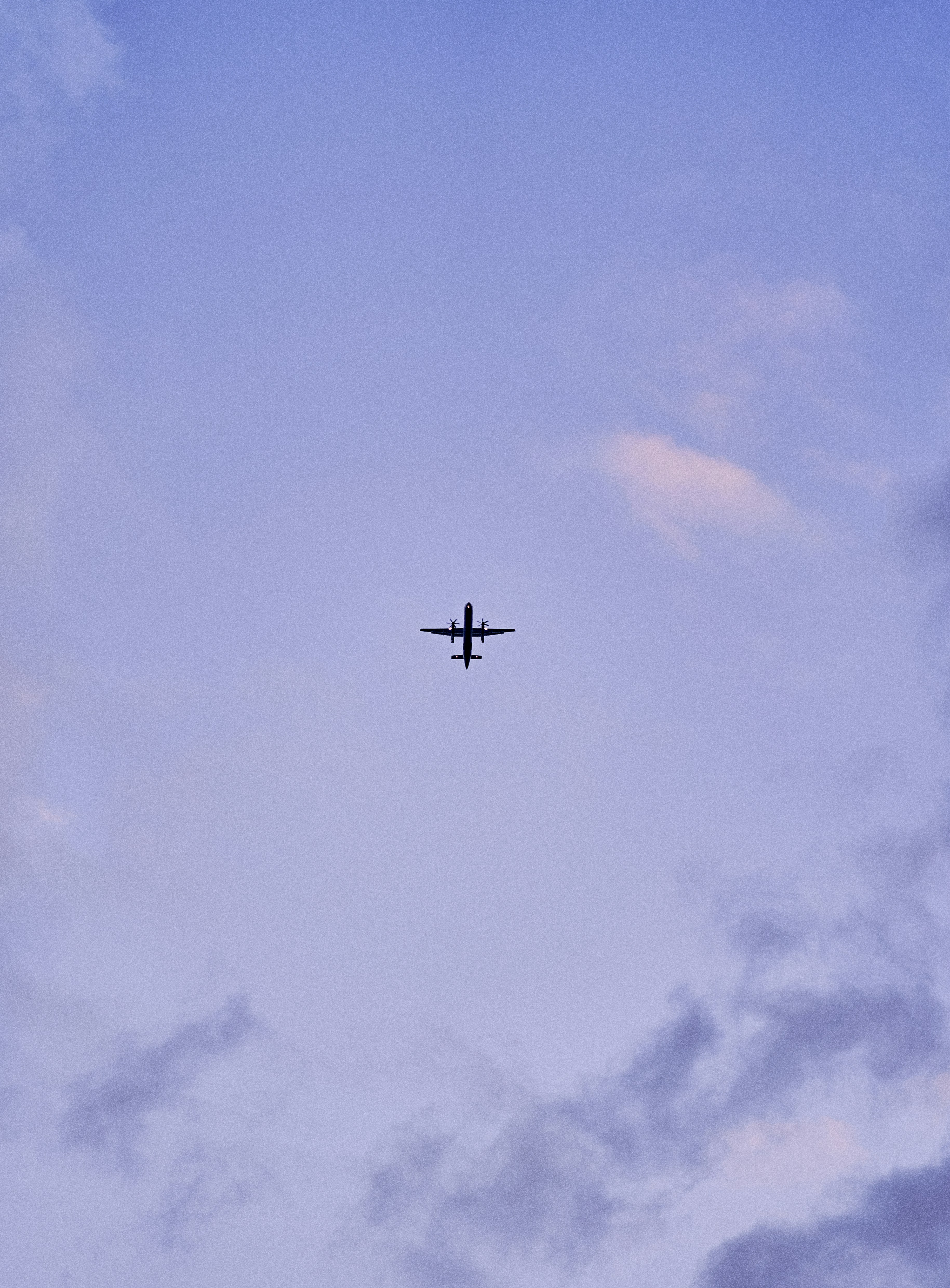 An airplane glides gracefully across a soft, pastel sky adorned with wispy clouds during twilight.