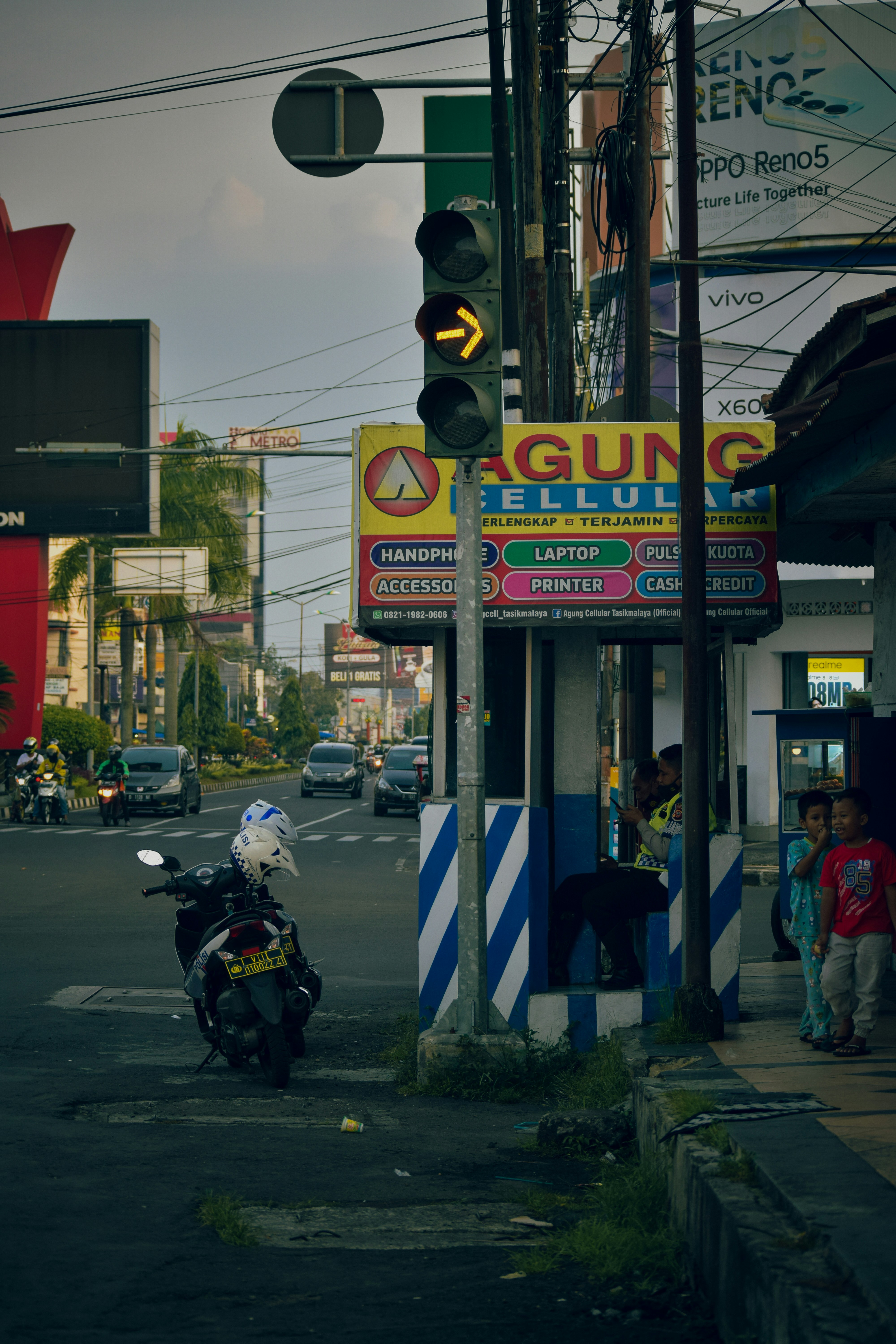 A busy street scene featuring a traffic light, a shop sign, and pedestrians interacting, showcasing urban life. The image captures the hustle and bustle of city living.