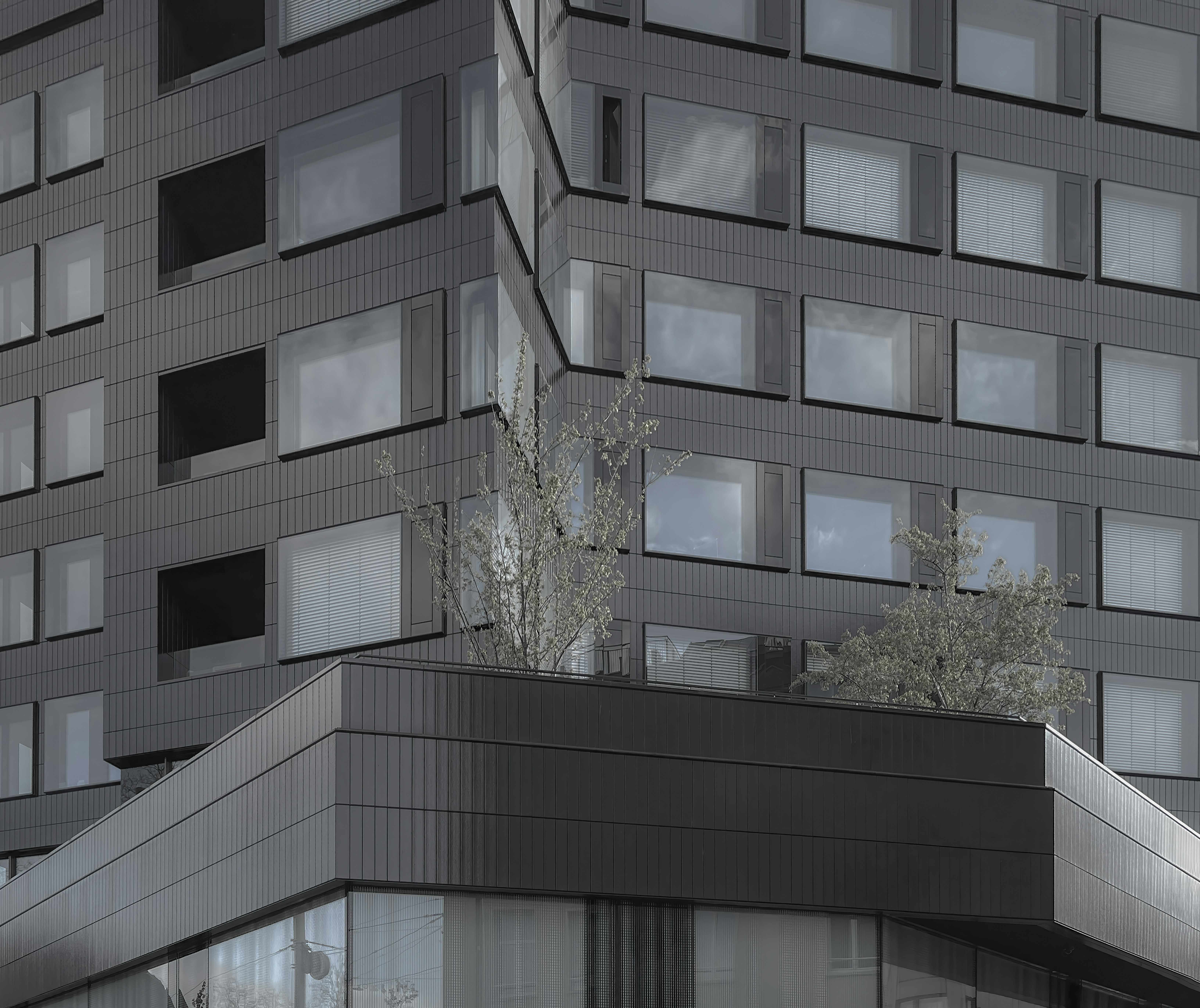 Modern architecture featuring a geometric facade with large windows and greenery atop a sleek structure.