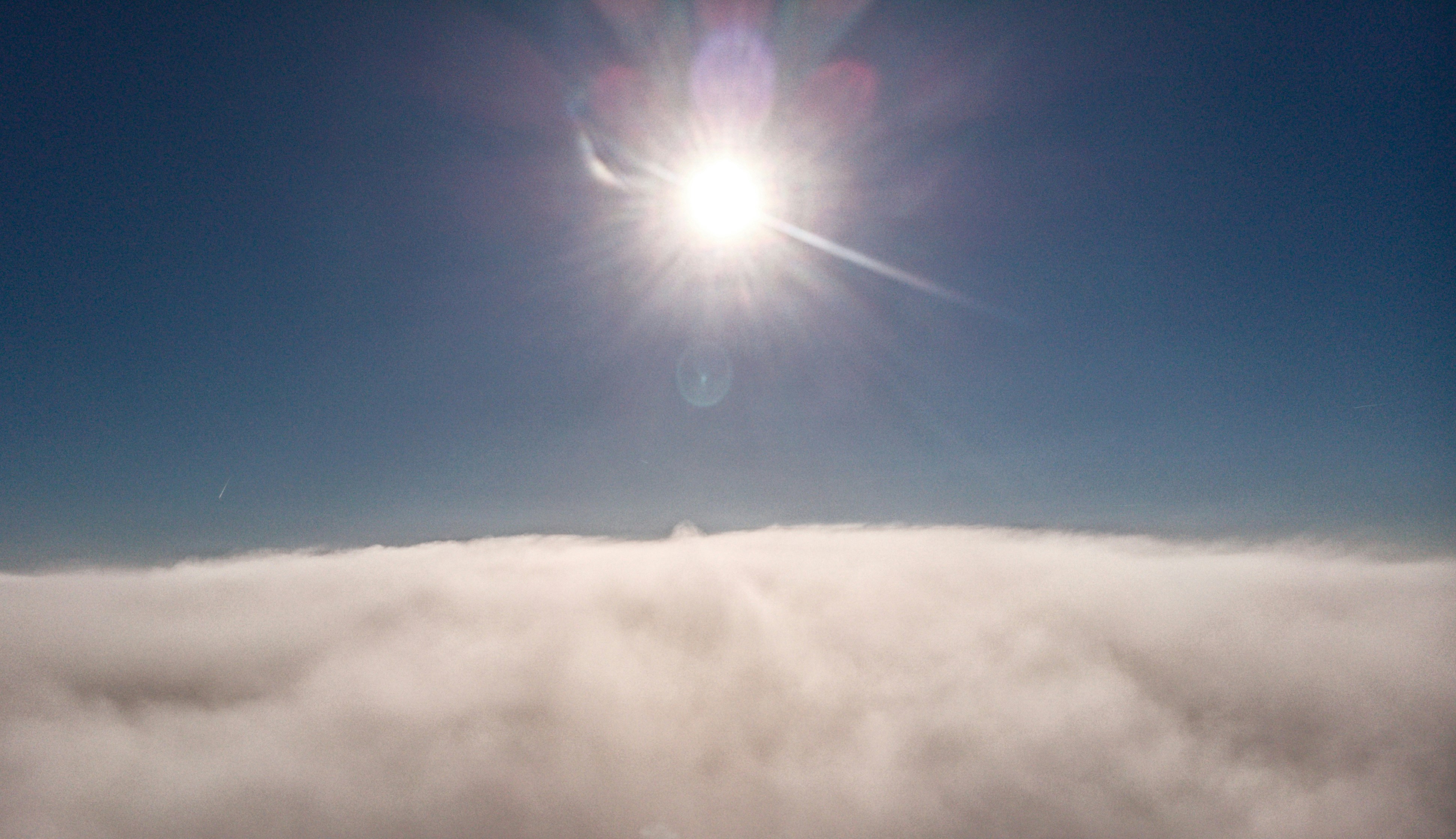 Bright sun illuminating a sea of clouds, creating a surreal aerial landscape. The vast expanse below adds depth to the celestial view.