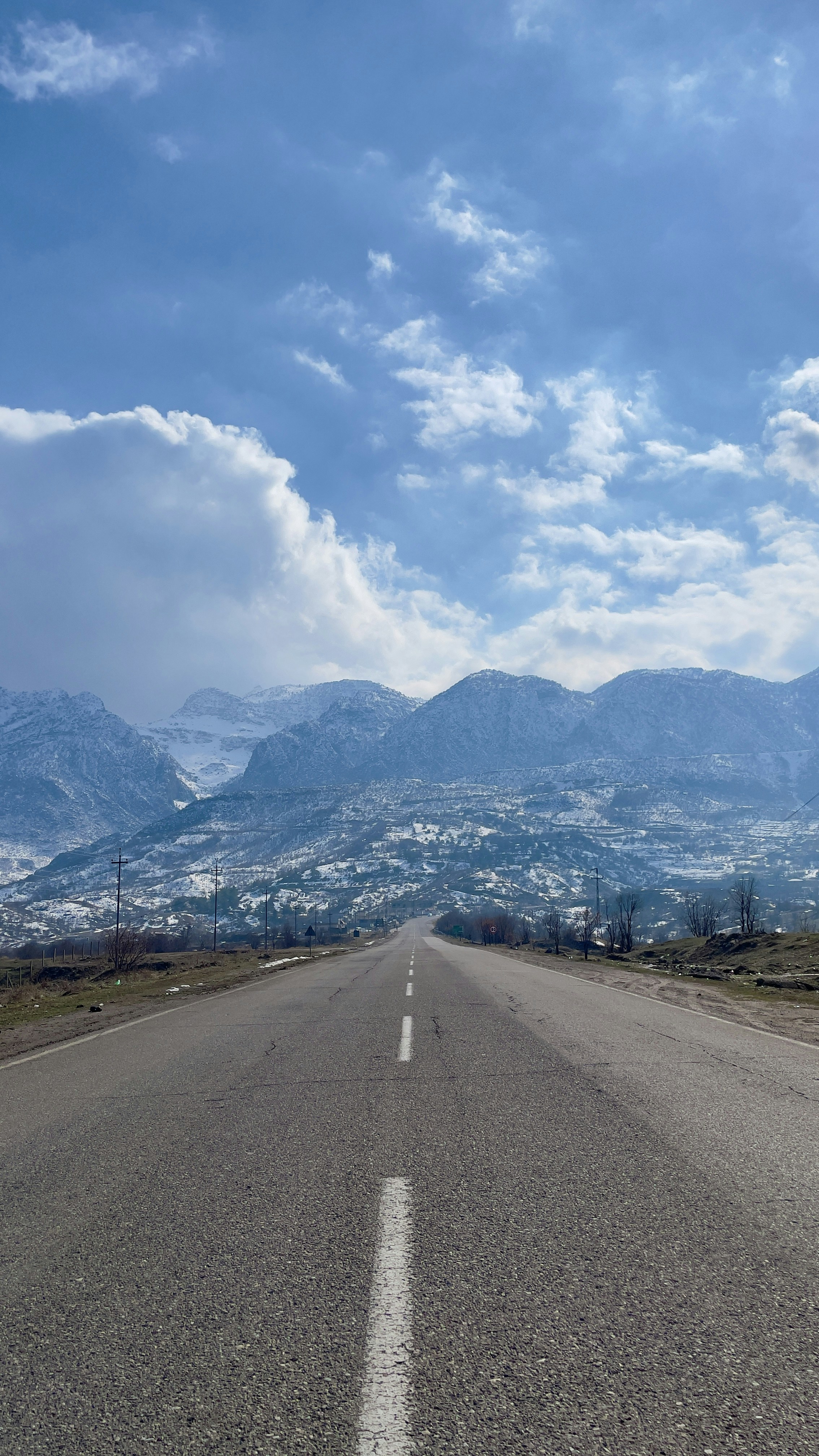 Winding road leading towards majestic snow-covered mountains under a partly cloudy sky.