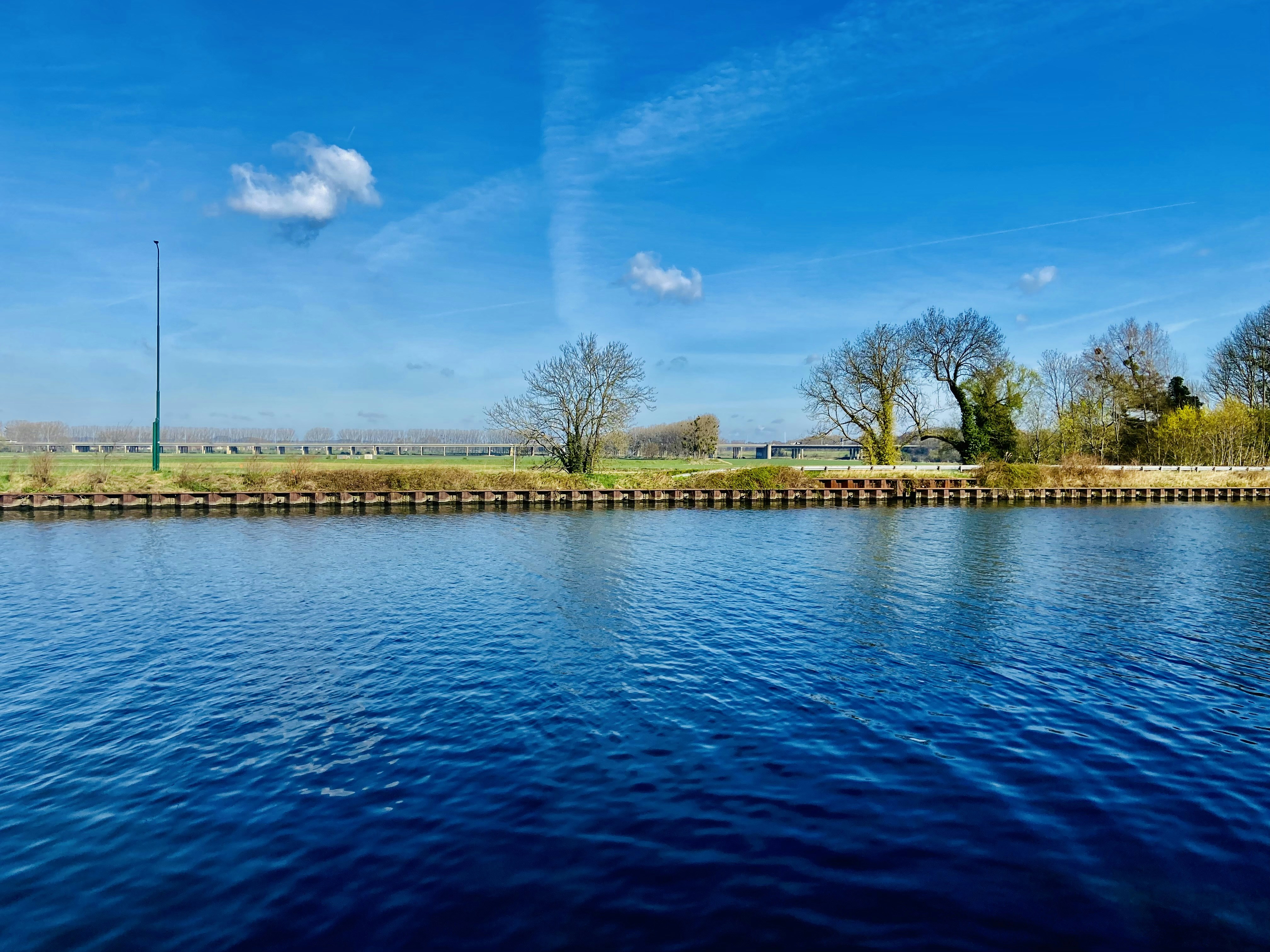 Serene waters reflecting a clear blue sky, bordered by trees and a distant fence line.