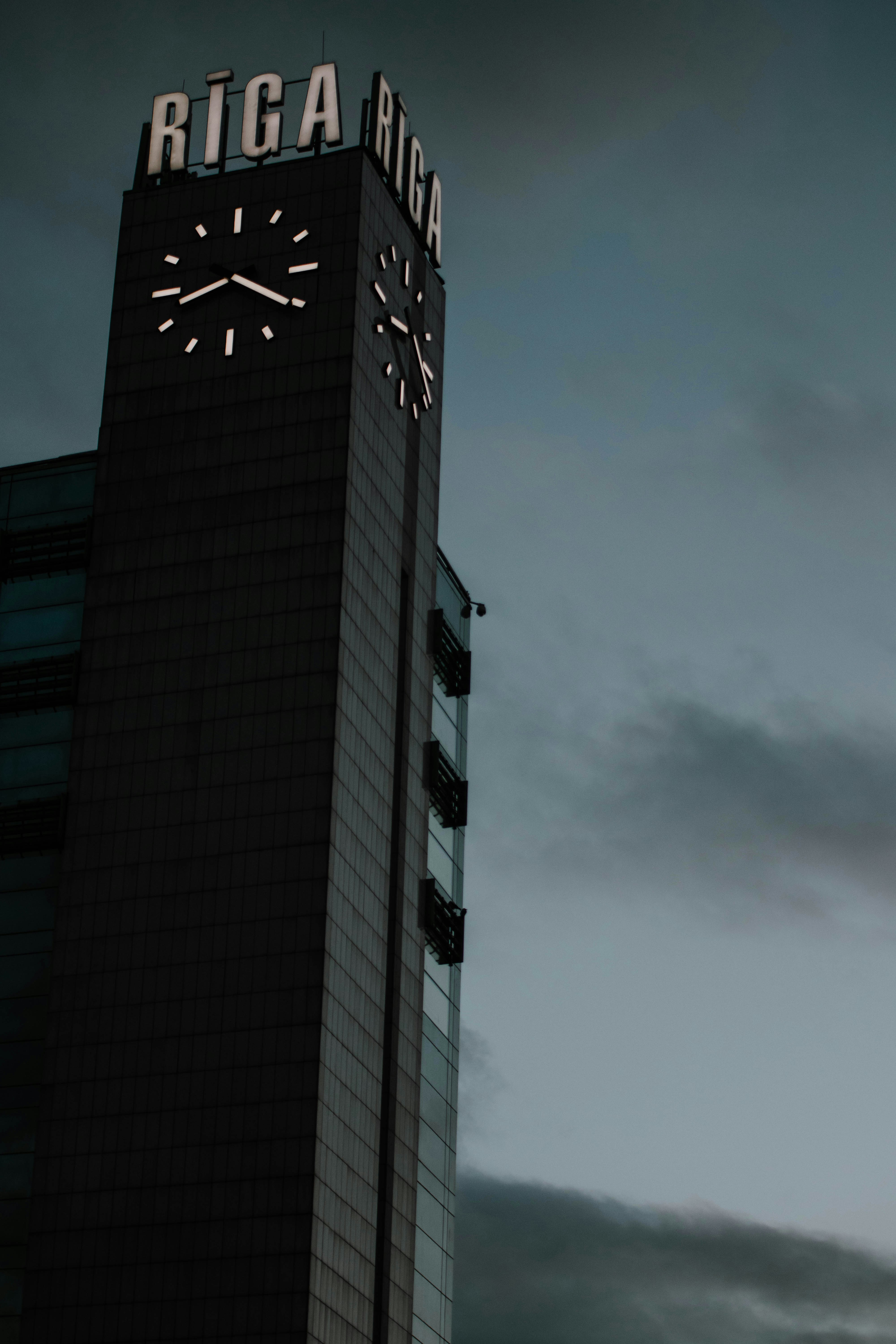 Illuminated clock tower of Rīga stands against a moody sky, showcasing its architectural elegance and the passage of time.